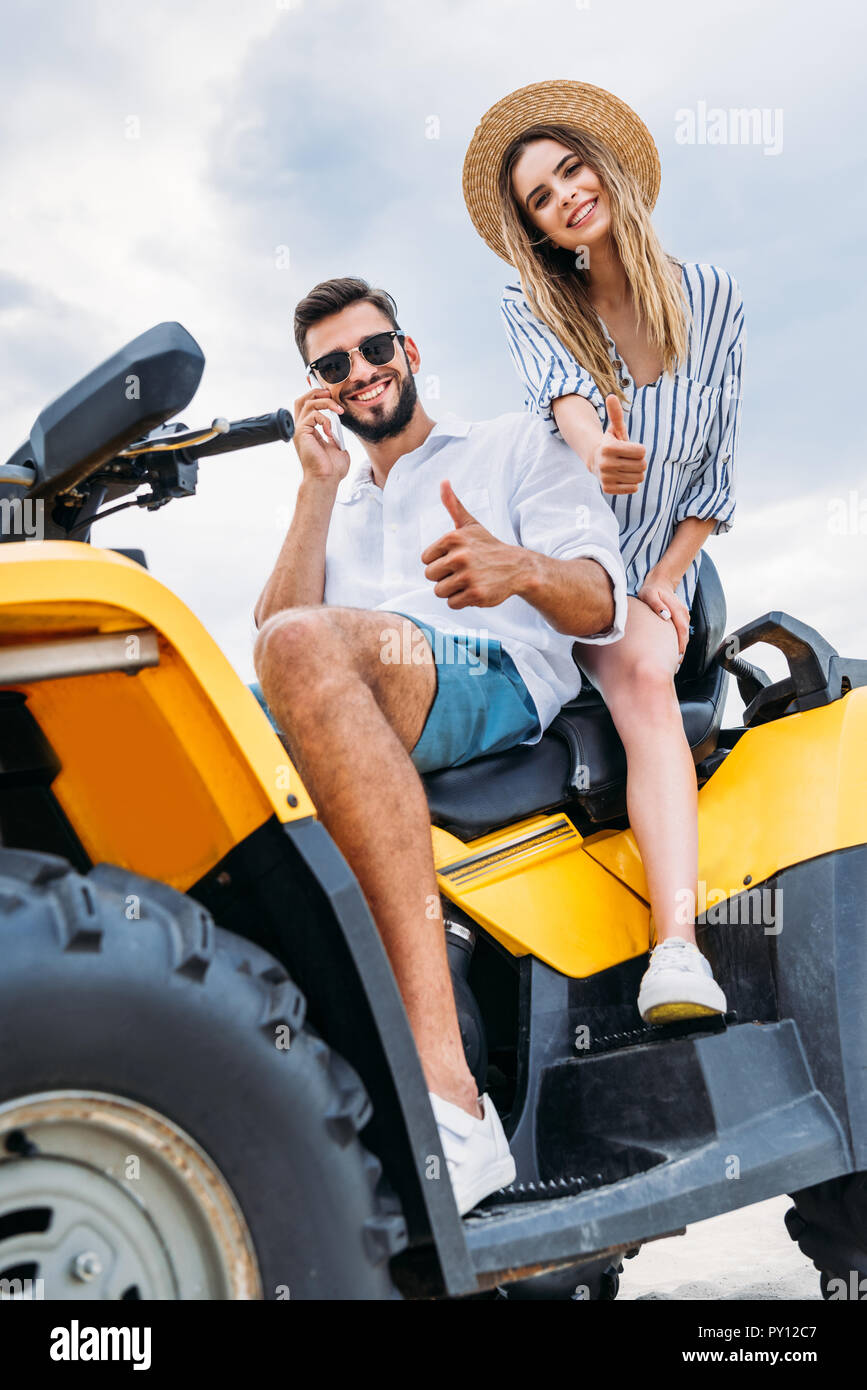 happy young couple sitting on ATV and showing thumbs up Stock Photo - Alamy