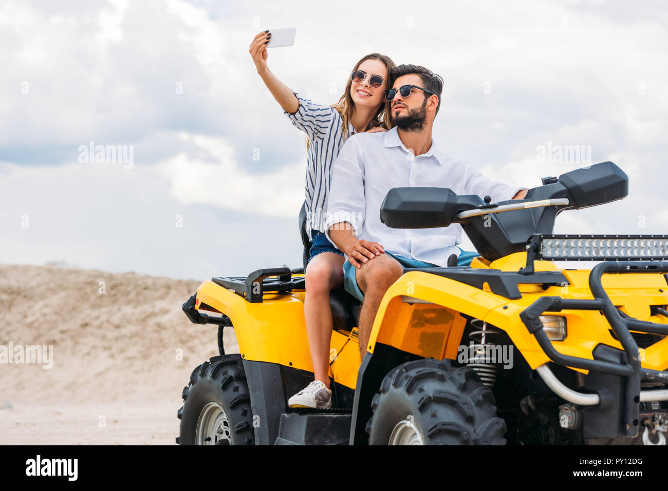 attractive young couple taking selfie while sitting on ATV in desert ...