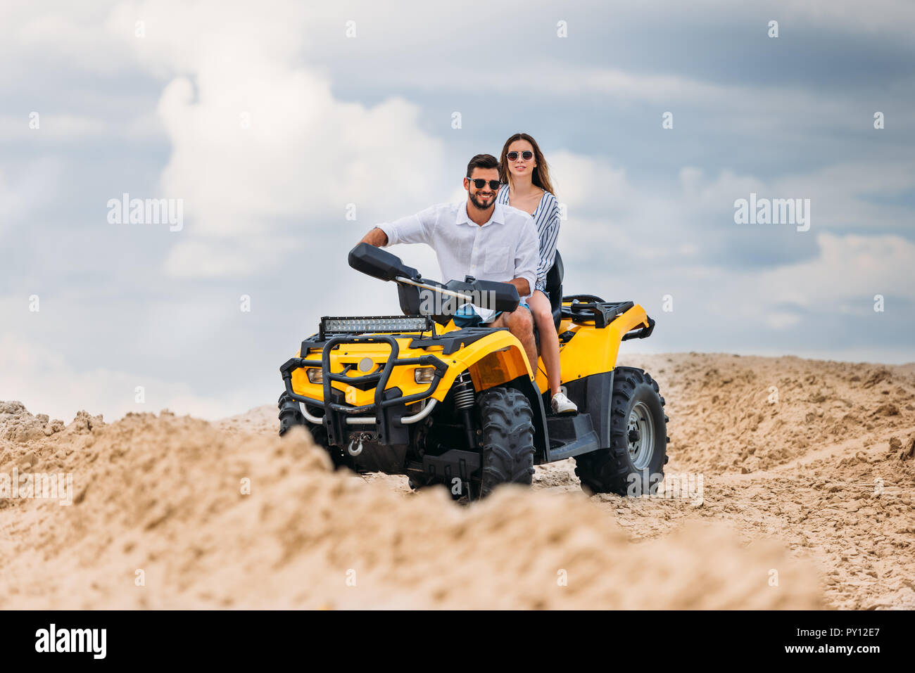 active young couple riding all-terrain vehicle in desert on cloudy day ...