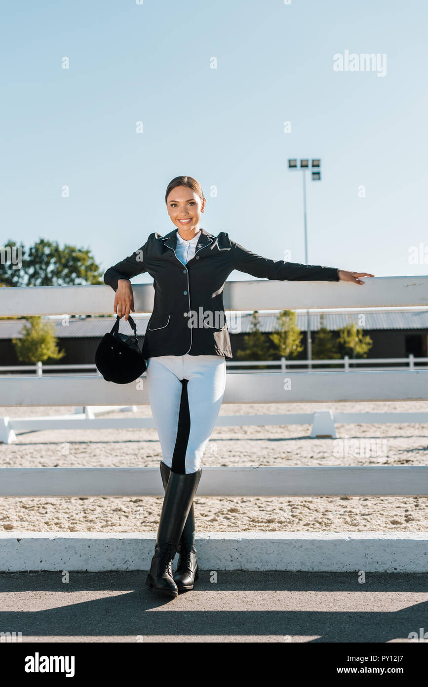 beautiful smiling female equestrian leaning on fence and looking at ...
