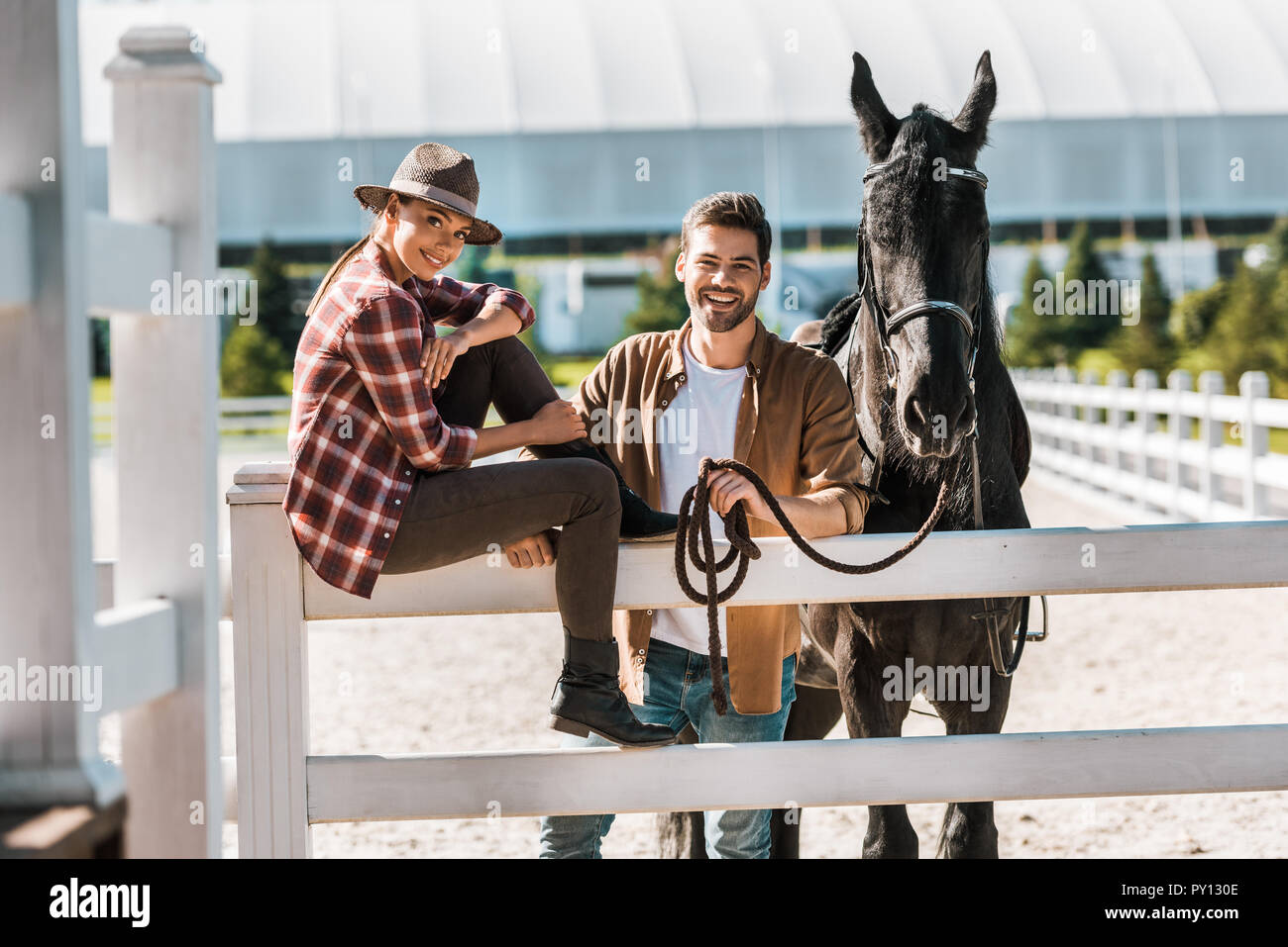 smiling female equestrian sitting on fence, colleague standing near ...