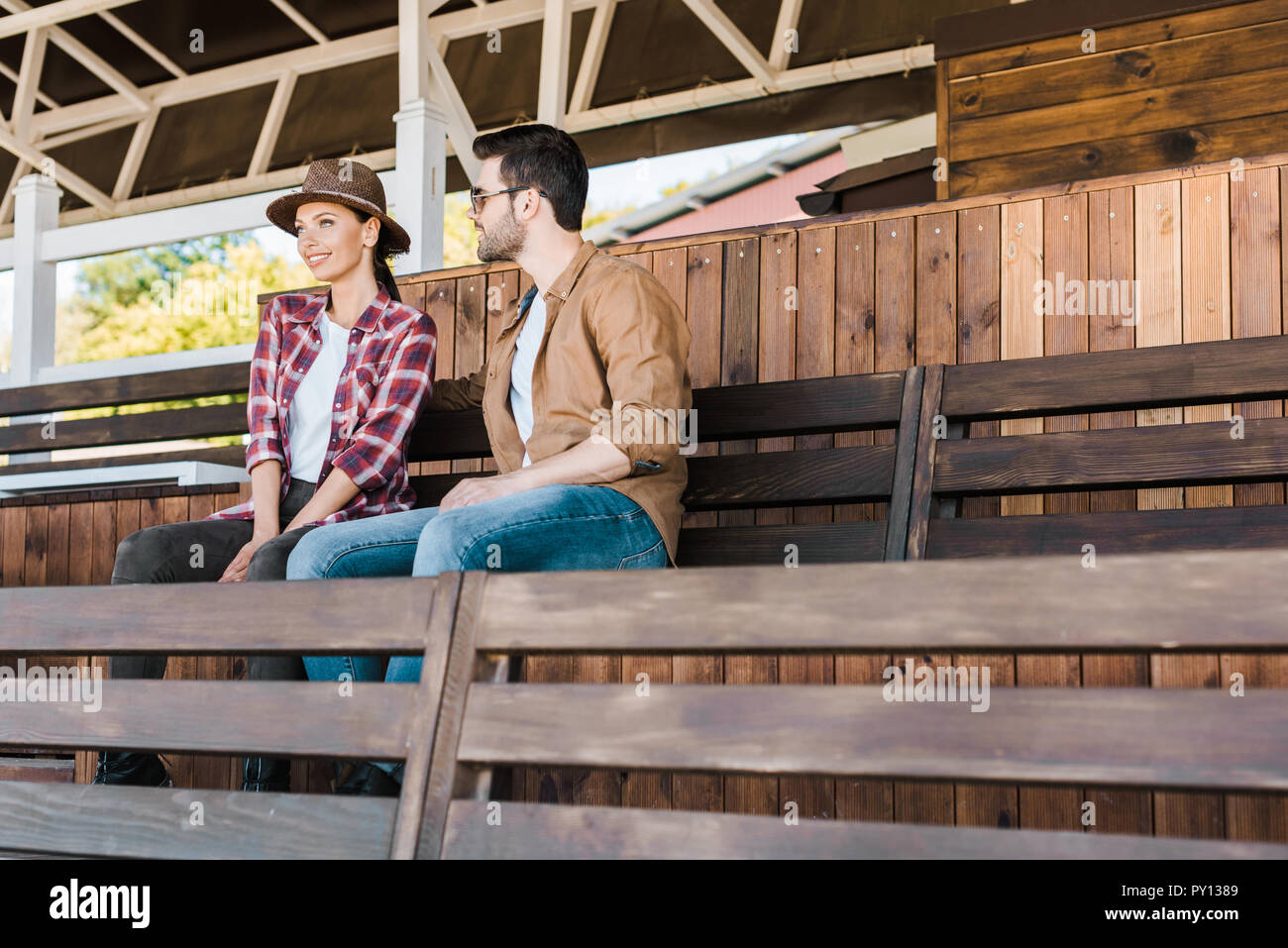 cheerful cowboy and cowgirl in casual clothes sitting on bench at ranch ...