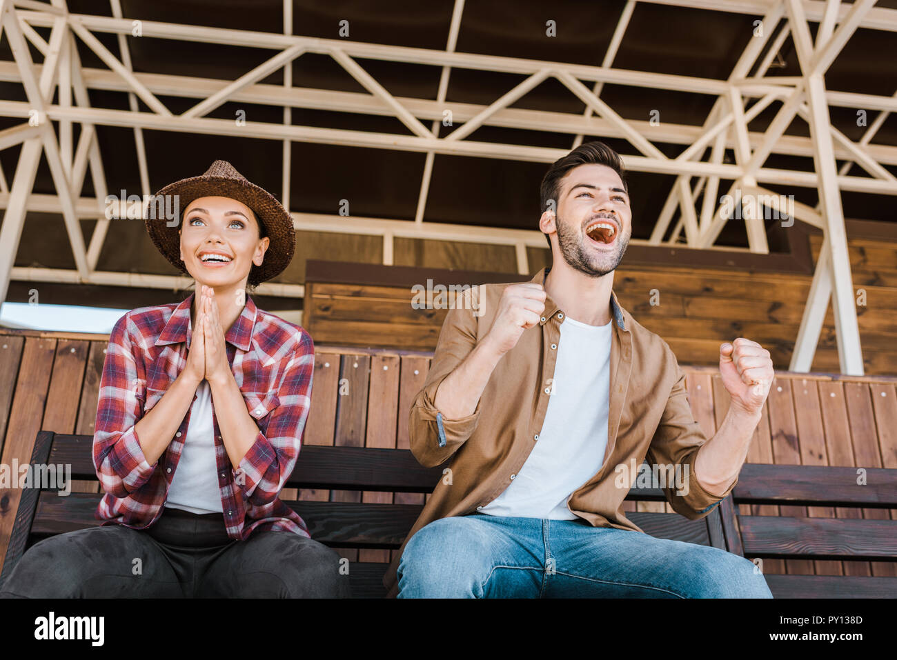 excited cowboy and cowgirl in casual clothes sitting on bench at ranch ...