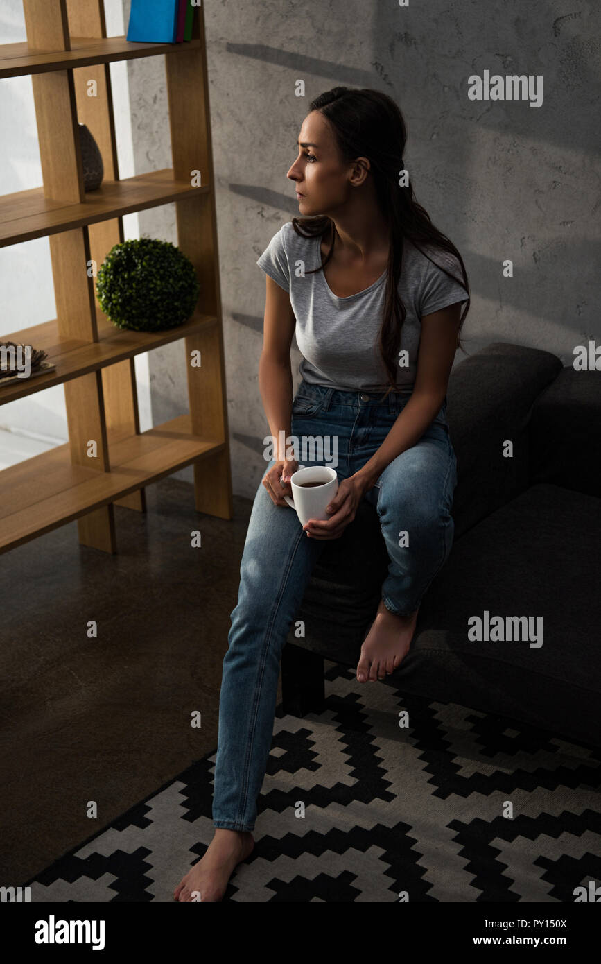 upset woman with cup of coffee sitting on sofa Stock Photo - Alamy