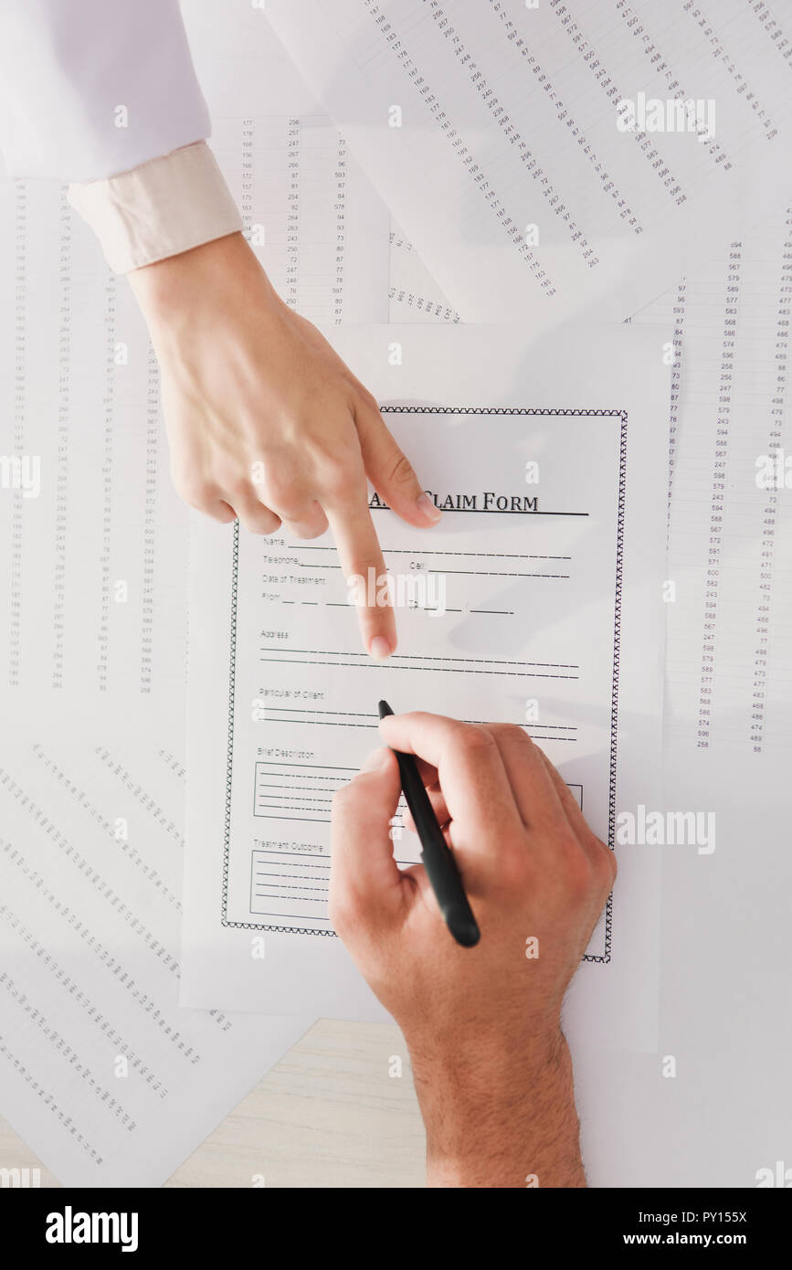 top view of man signing insurance claim form while doctor pointing at ...