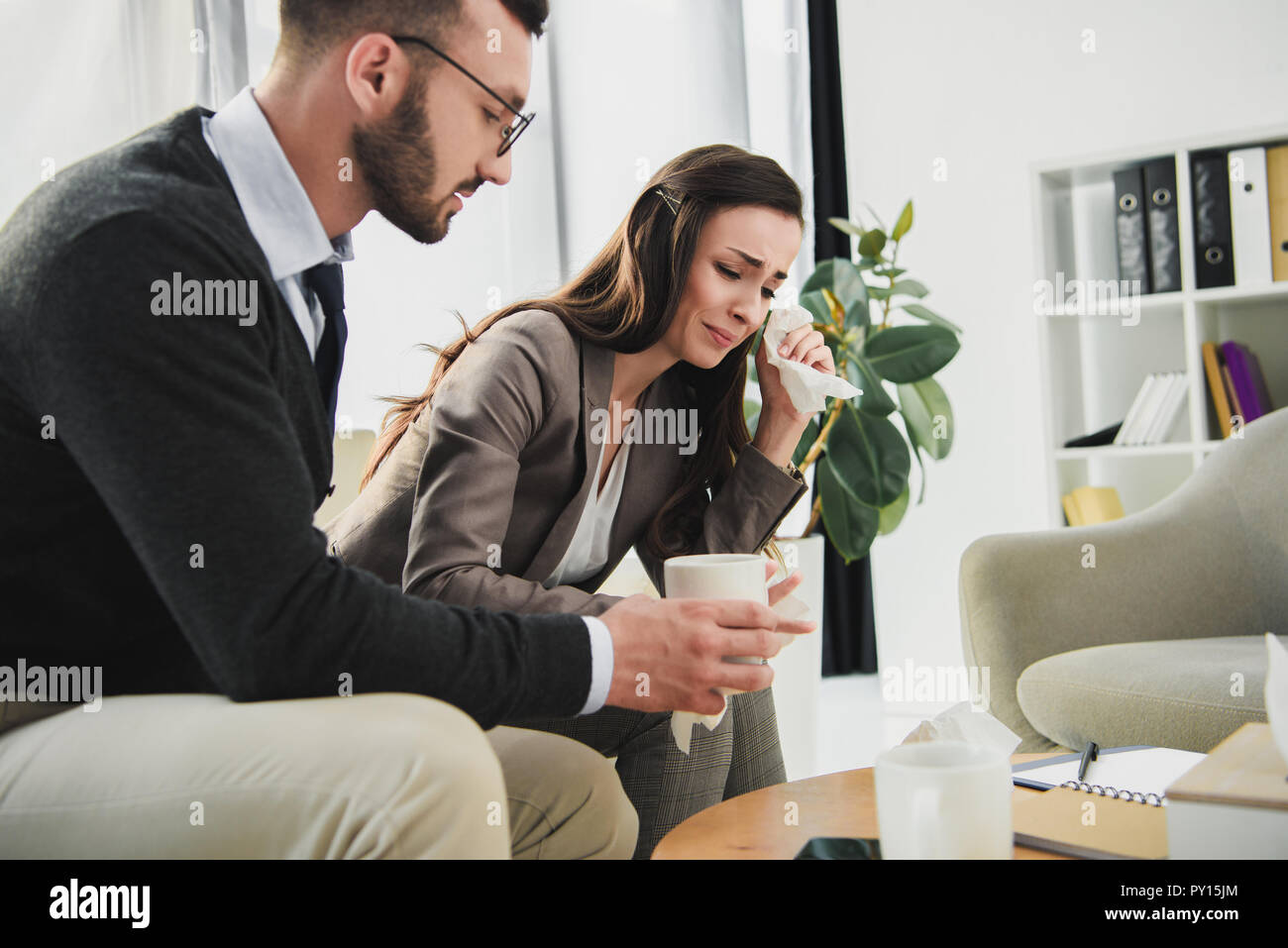 psychologist giving cup of tea to crying patient in doctors office ...