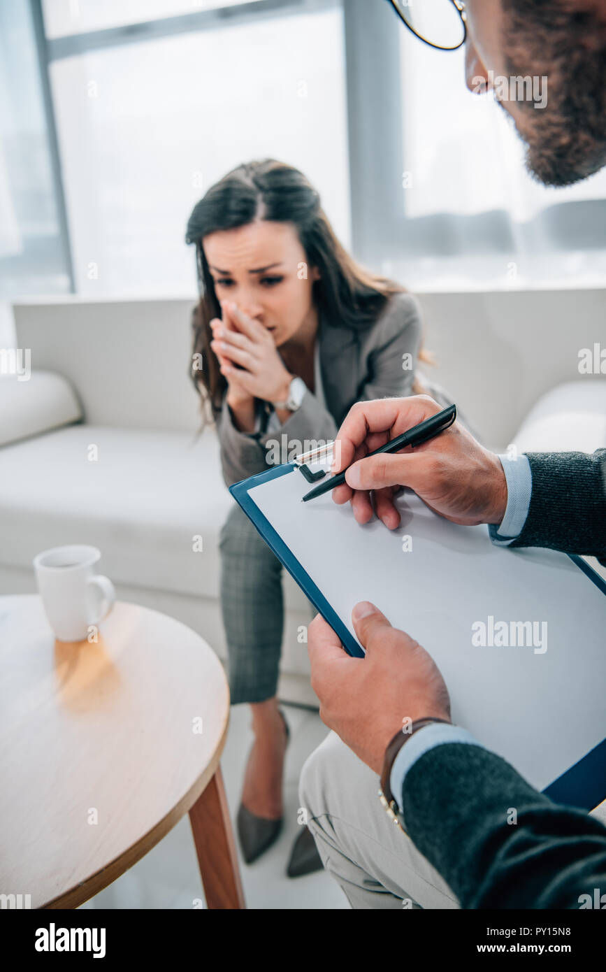 cropped image of psychologist taking notes and sad patient looking down ...
