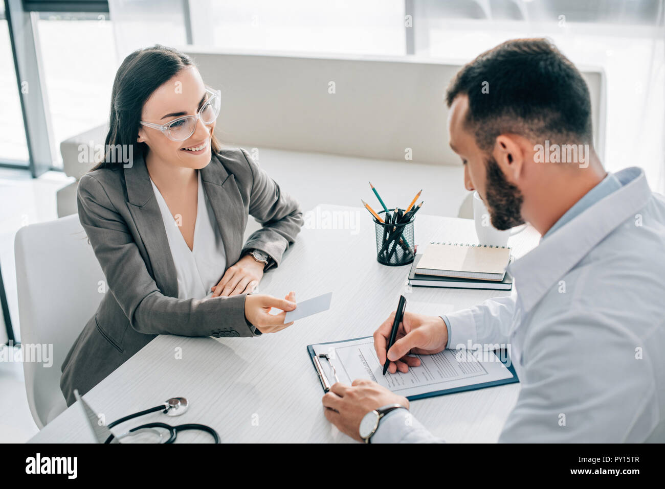 high angle view of smiling patient giving id card to doctor to fill ...