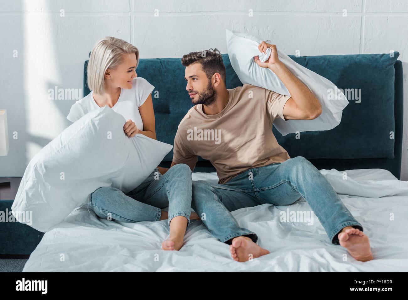 cheerful boyfriend and girlfriend fighting with pillows on bed in ...
