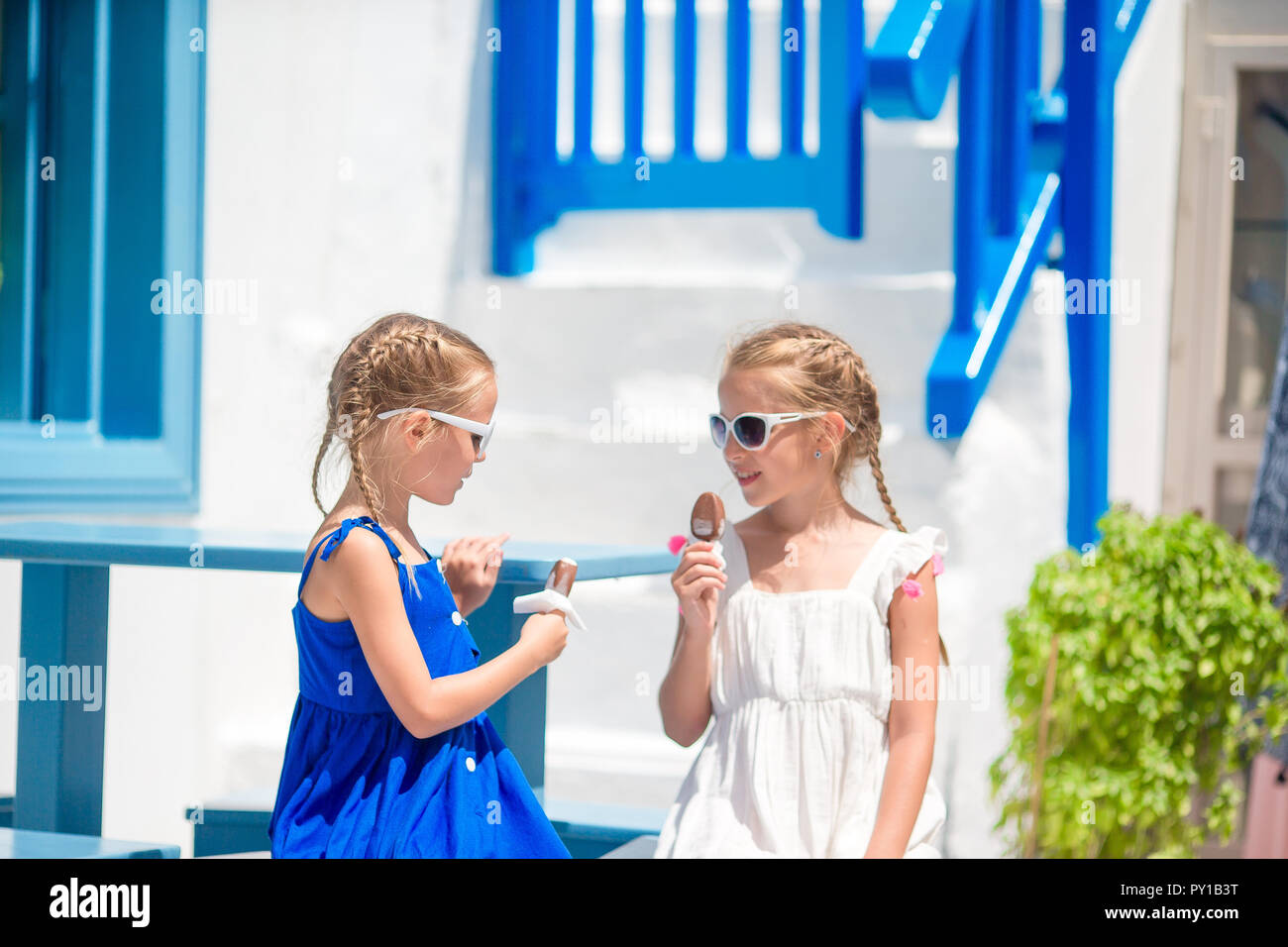 Two girls in blue dresses sitting on blue chairs and table on street of ...