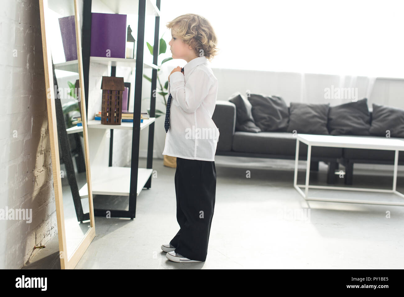side view of little boy tying necktie over white shirt in front of ...