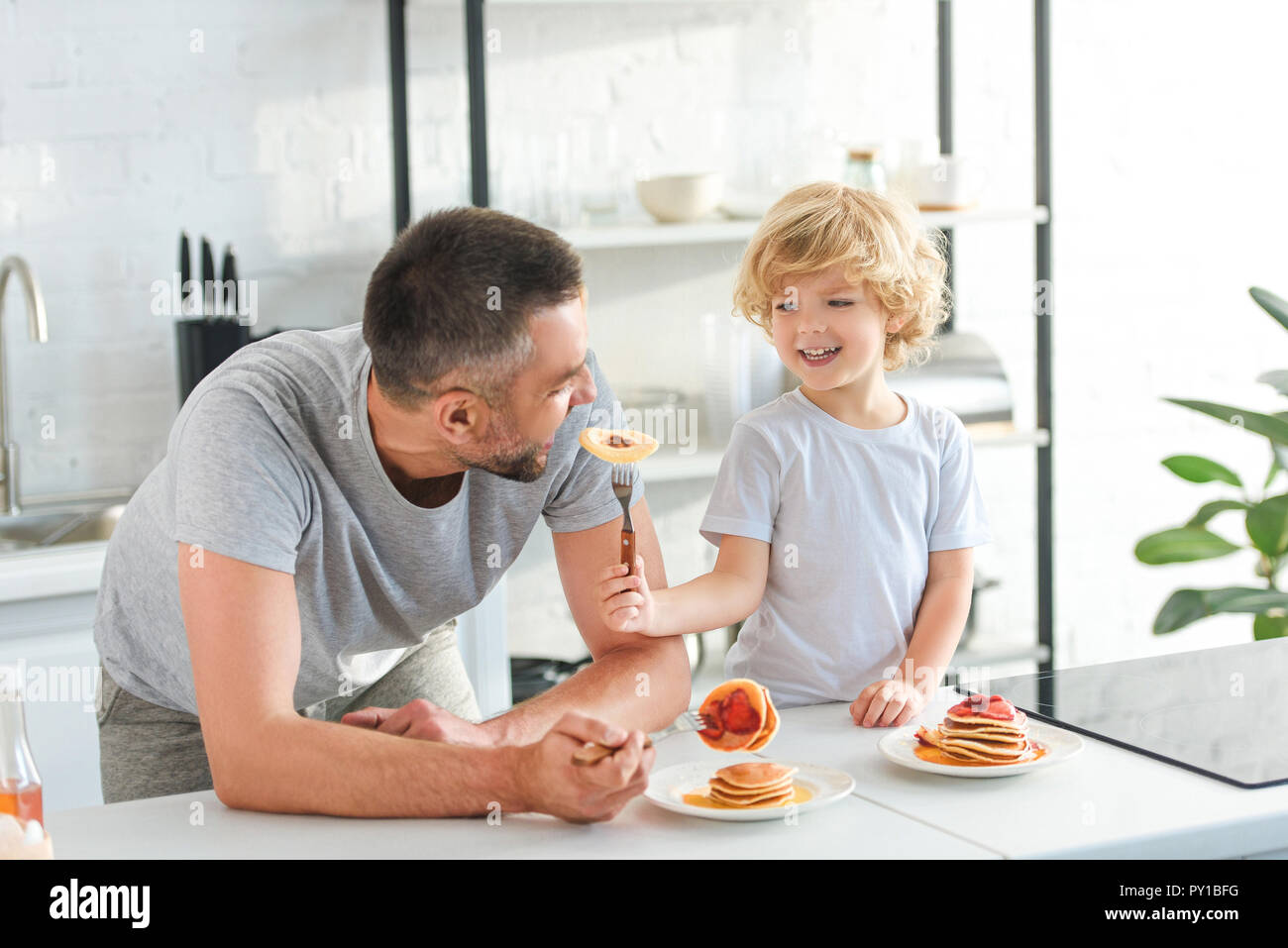 happy little boy feeding father by pancake at kitchen Stock Photo - Alamy