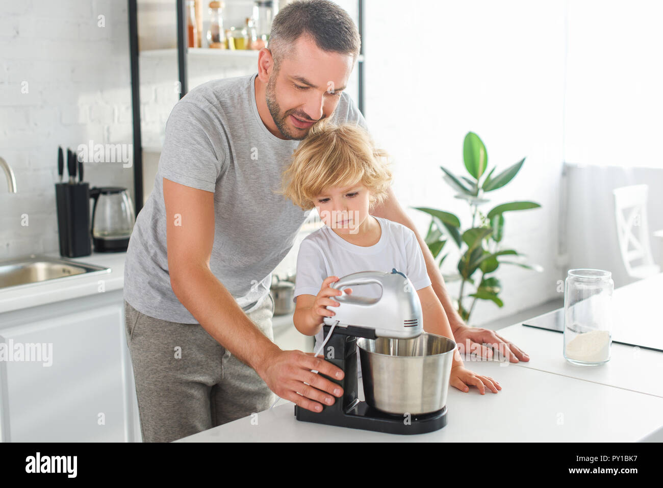 smiling man helping his son using mixer for making dough at kitchen ...