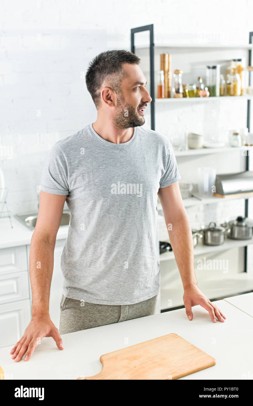 side view of adult man standing near table with cutting board on ...