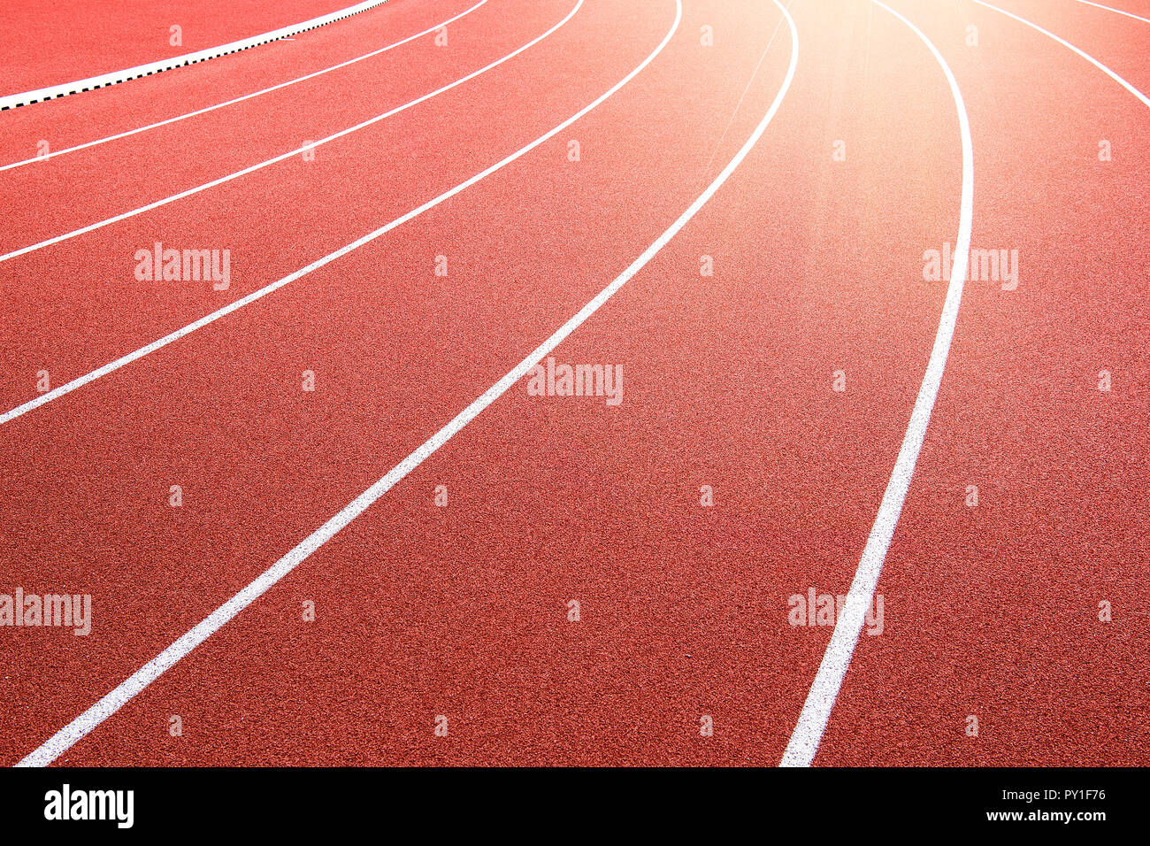 Curved white lines on a red running track with sunlight at the and of ...