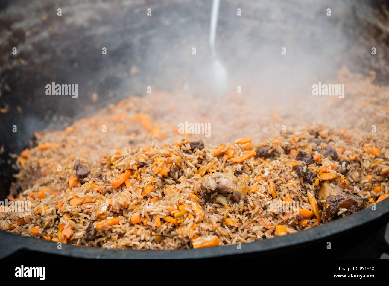 Tasty Uzbek pilaf in a cauldron on fire in the open air at street food ...