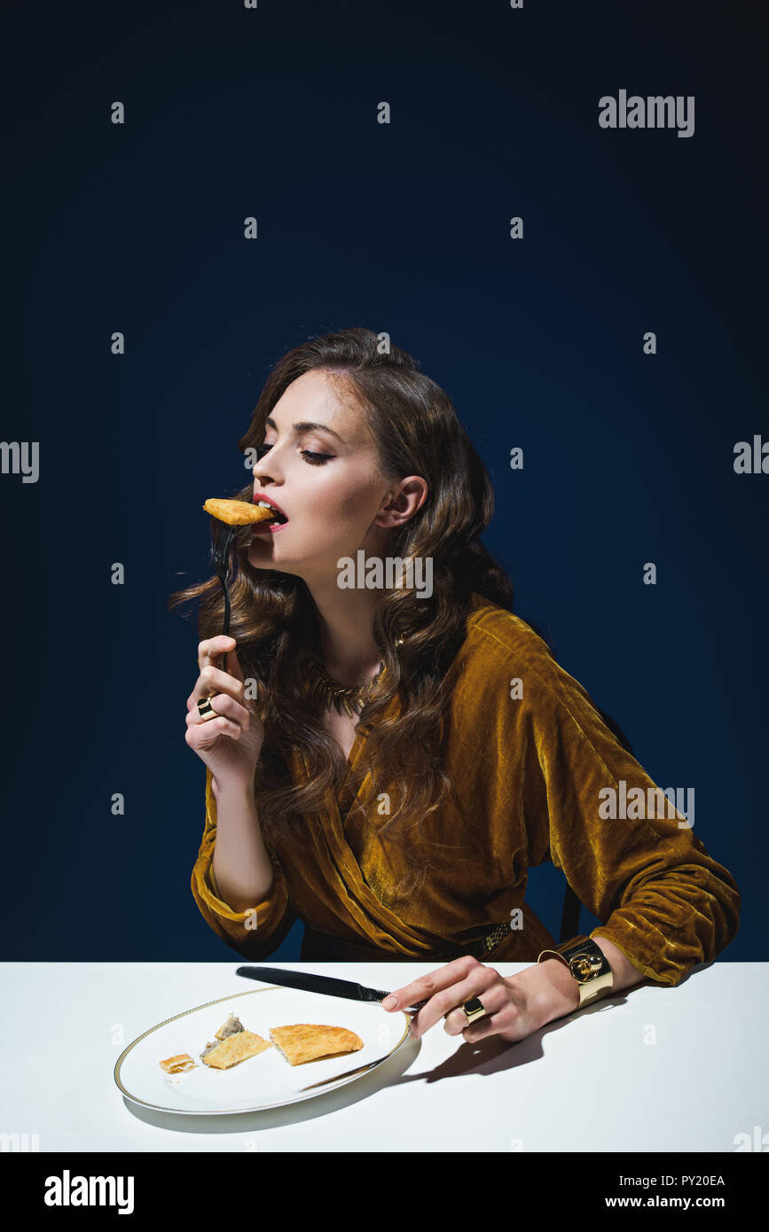 beautiful woman in stylish clothes eating meat pastry at table with ...