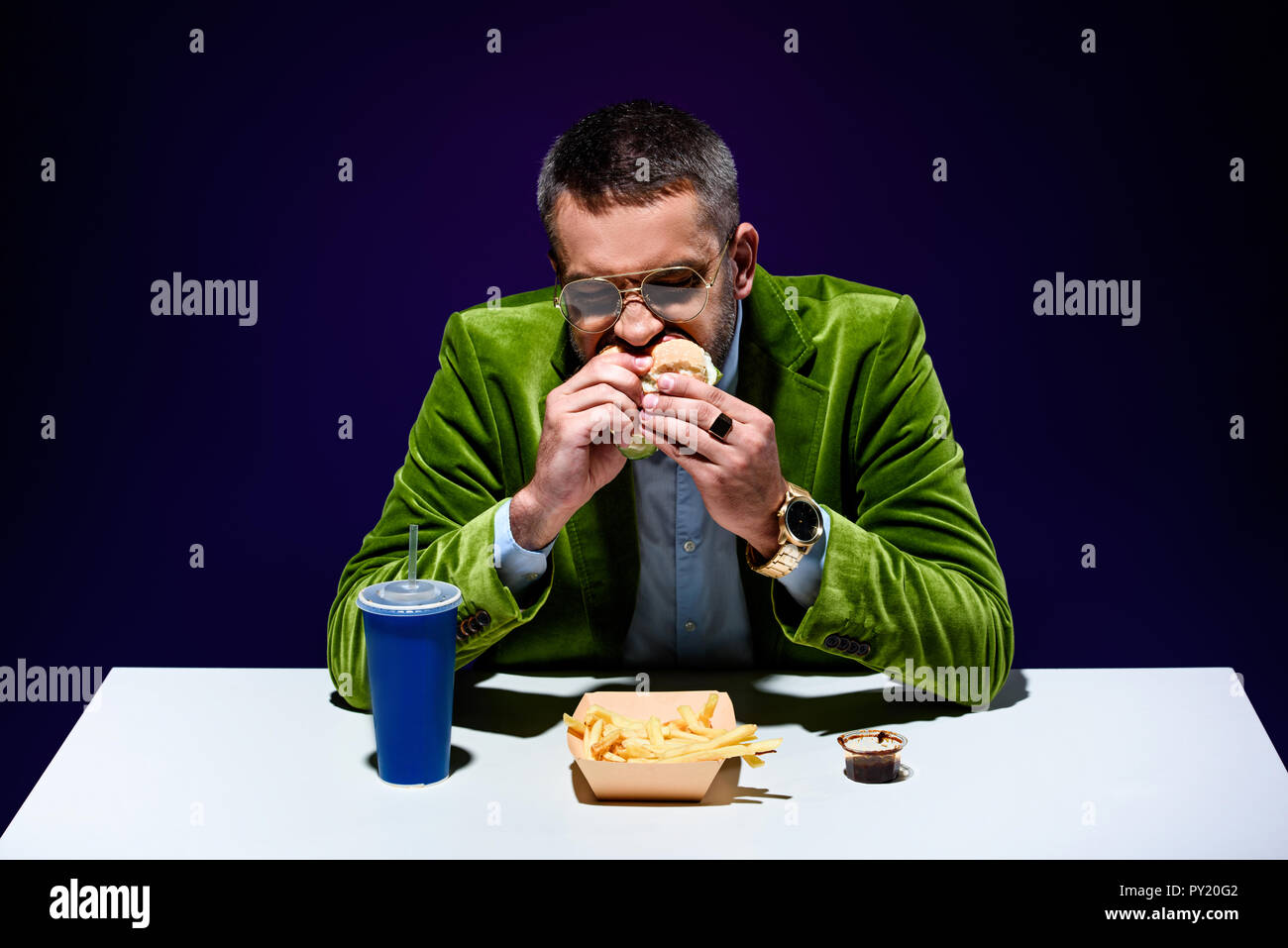 portrait of man in velvet jacket eating burger at table with french ...