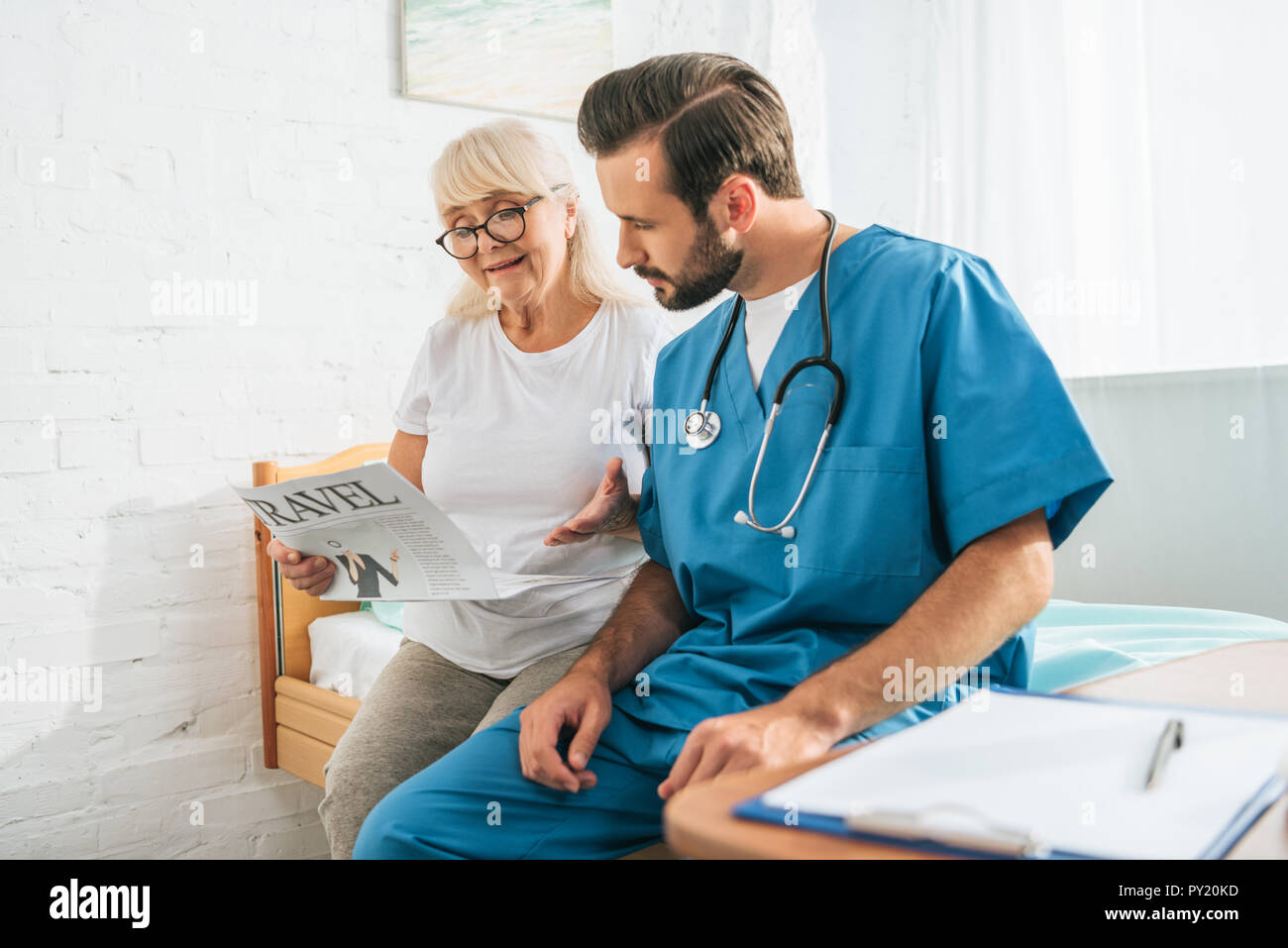 young doctor with stethoscope looking at senior woman reading travel ...