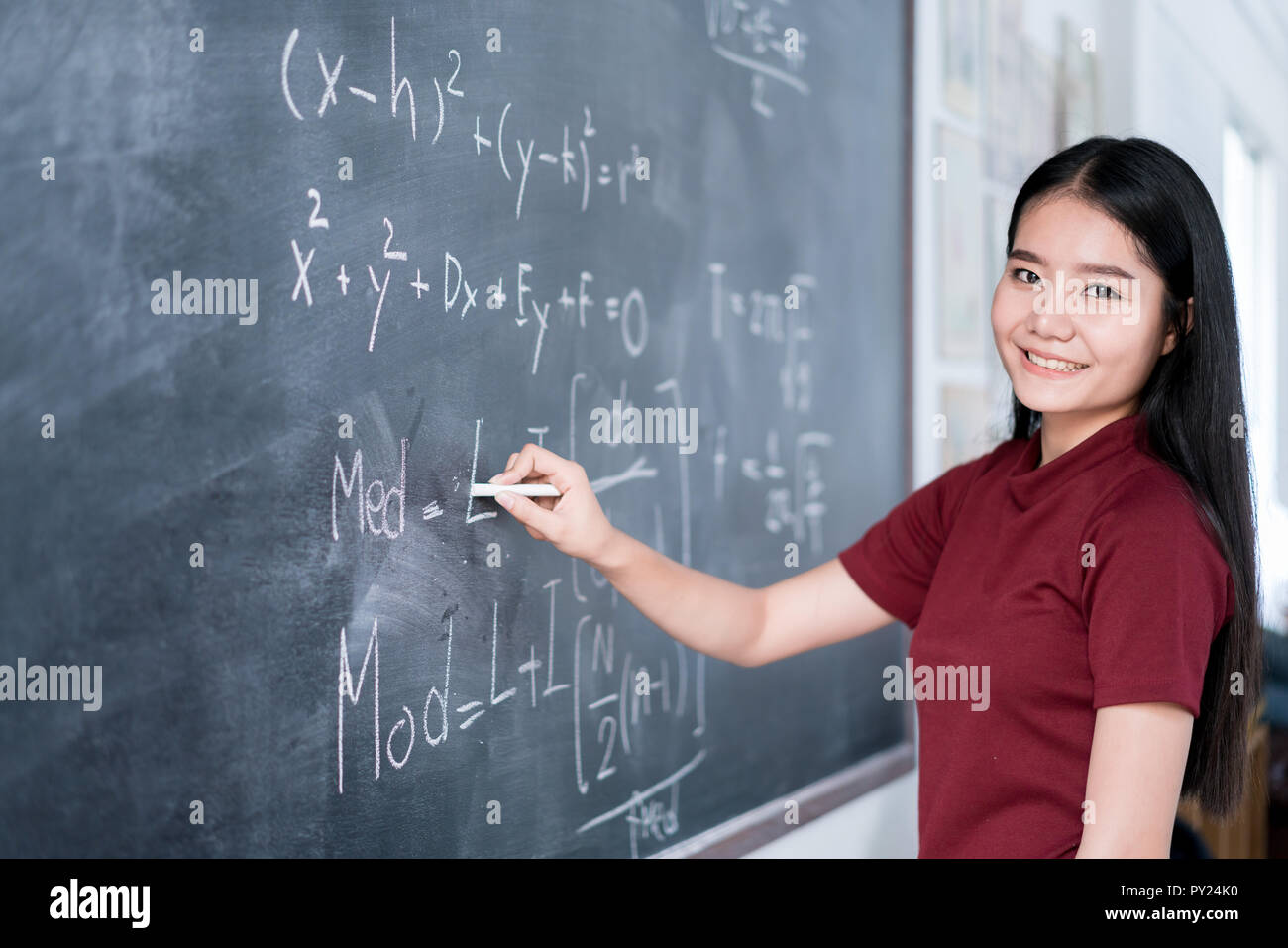 Beautiful Asian student writing on blackboard with chalk in classroom ...