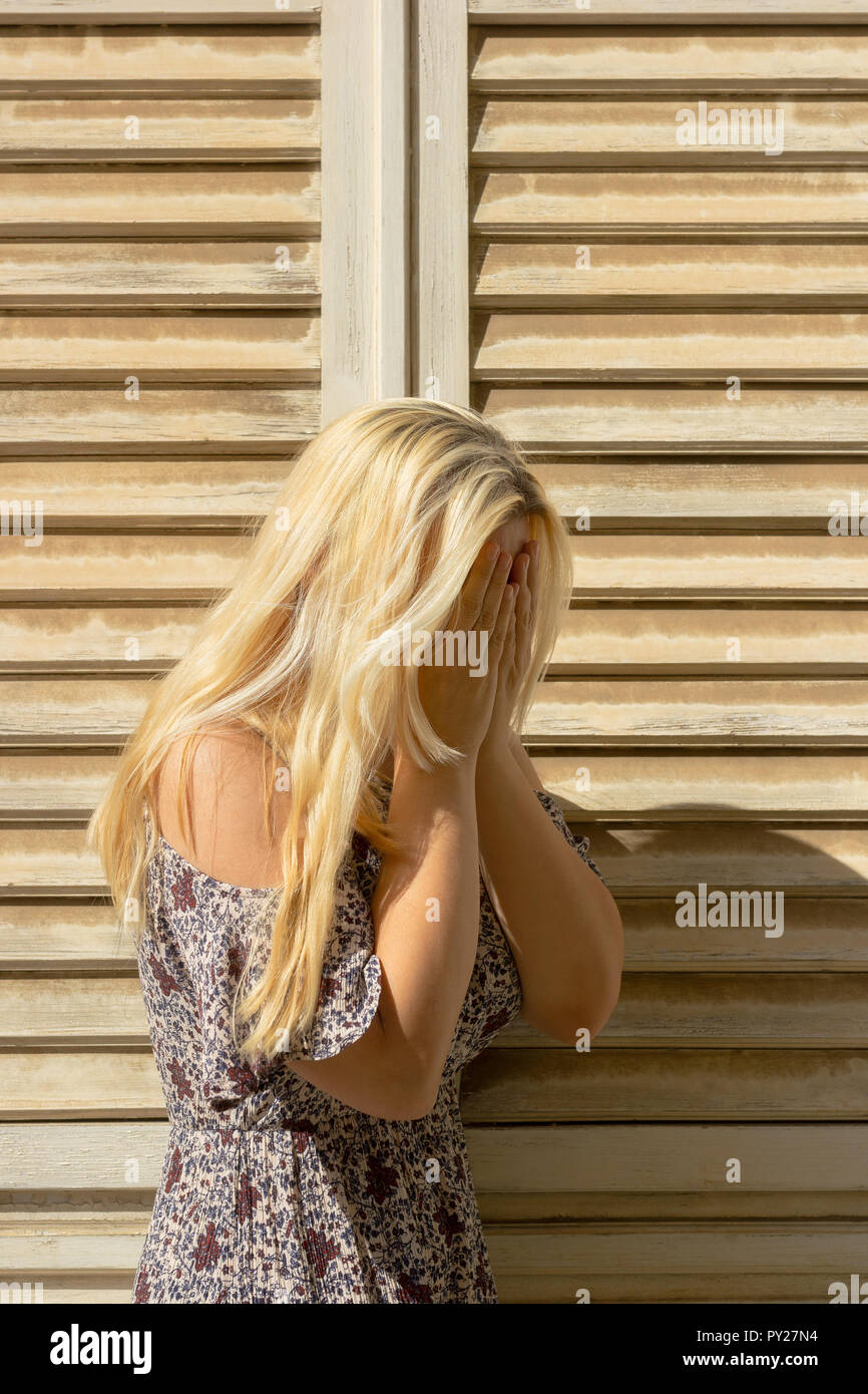 Blonde woman covering her face with hands and crying in front beige ...