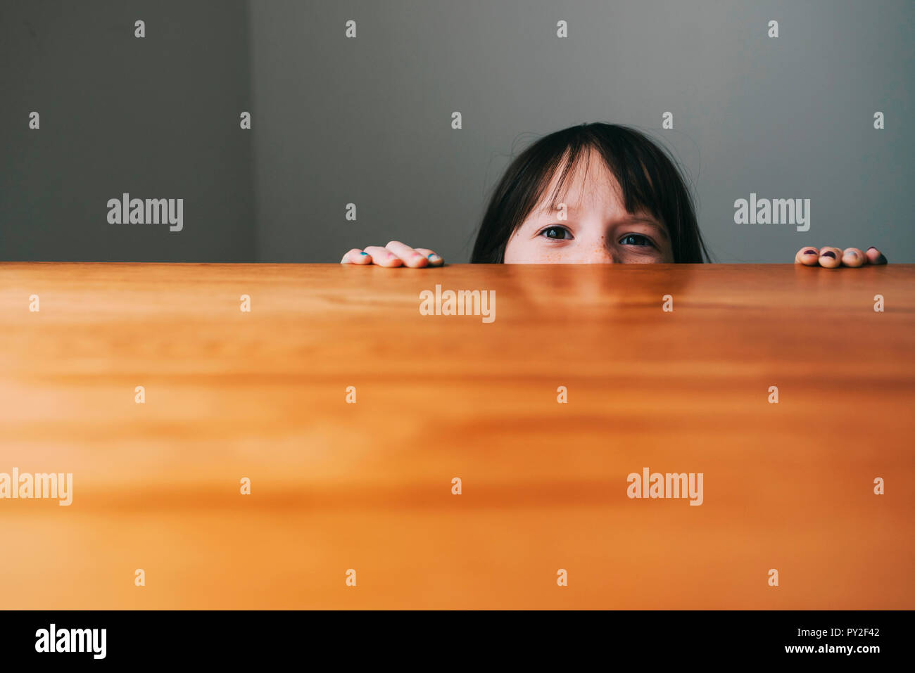 Girl hiding behind a table Stock Photo - Alamy