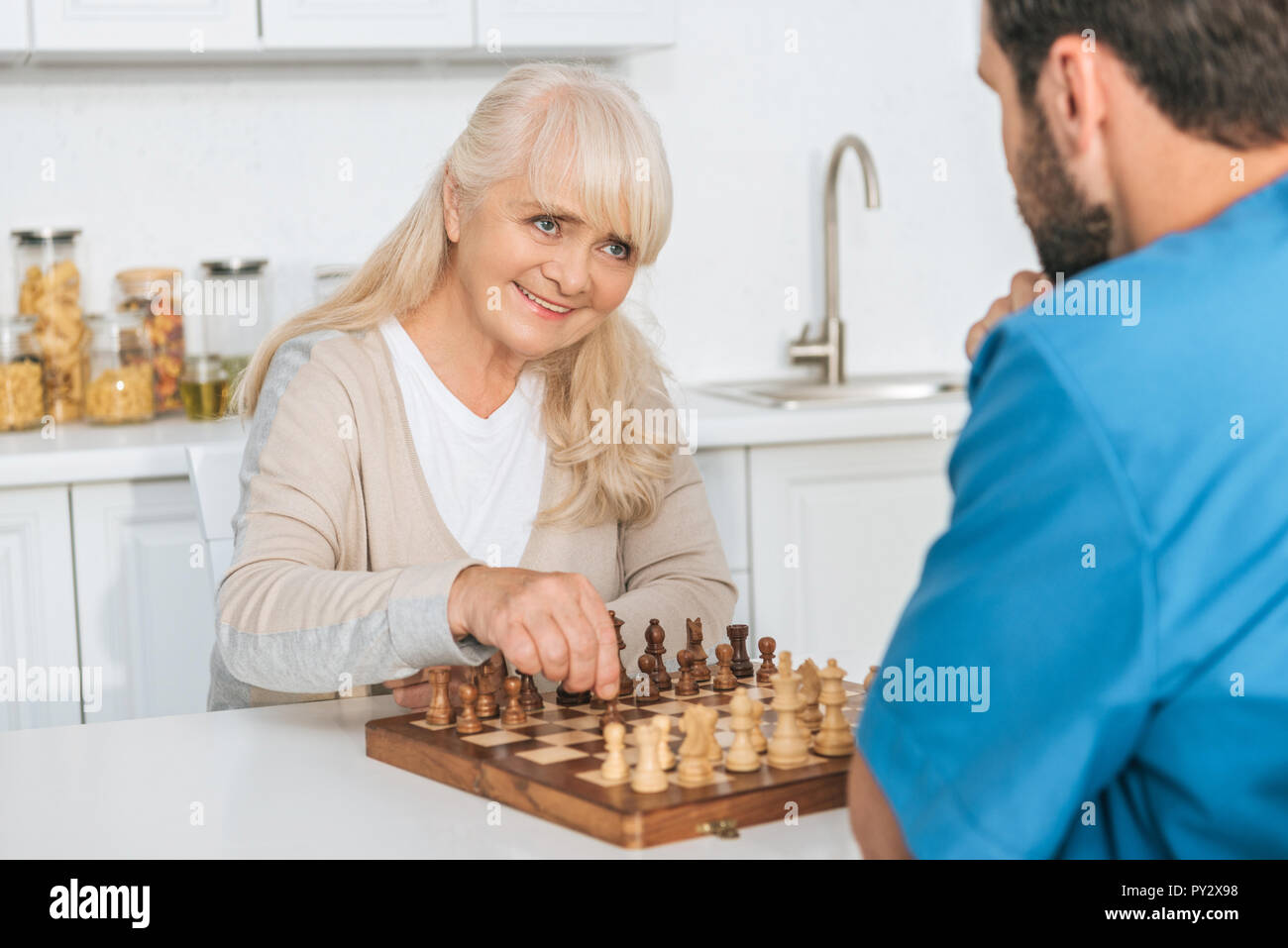 smiling senior woman playing chess with young male nurse Stock Photo ...