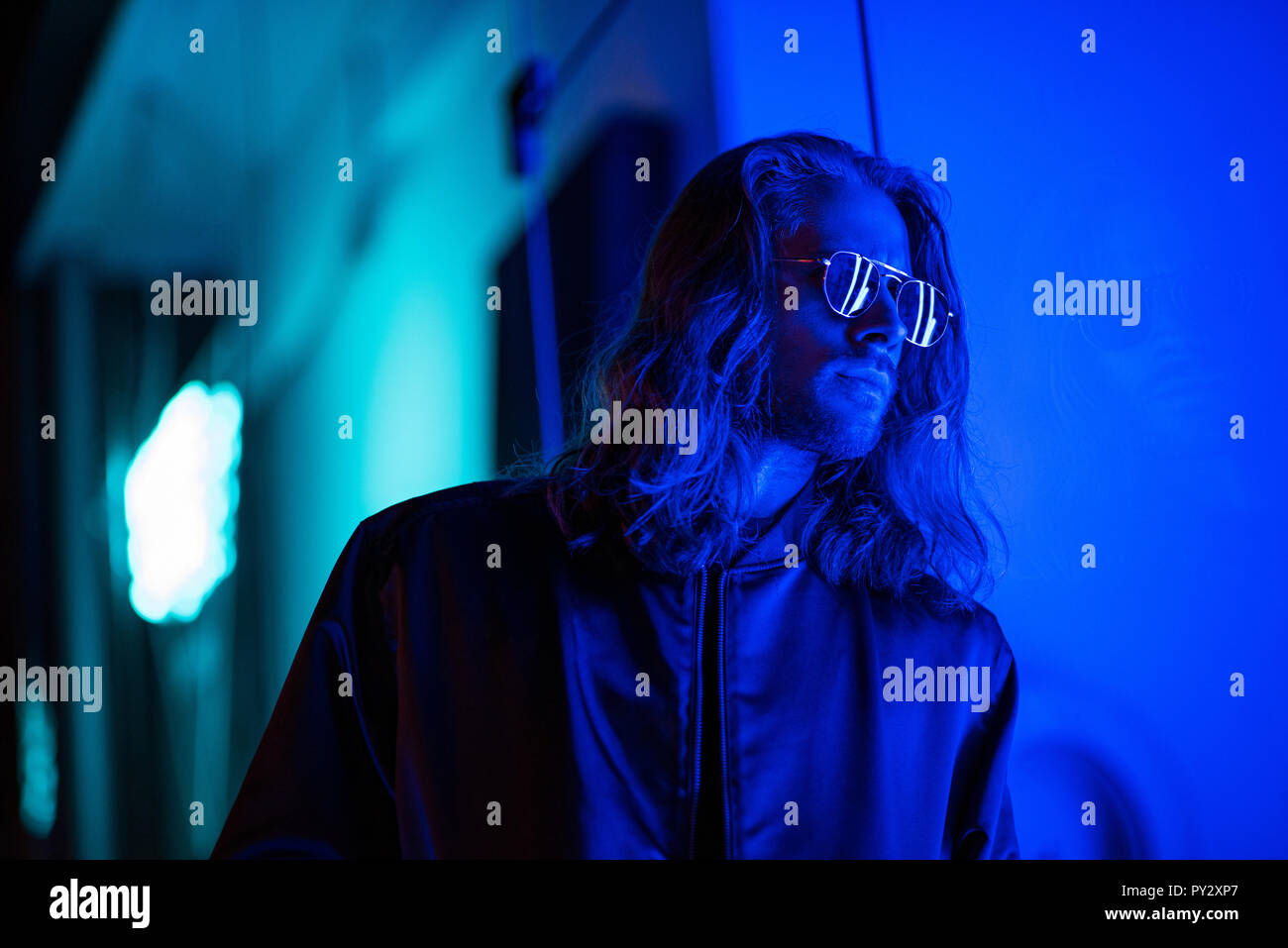 handsome young man in sunglasses under blue light on street at night ...