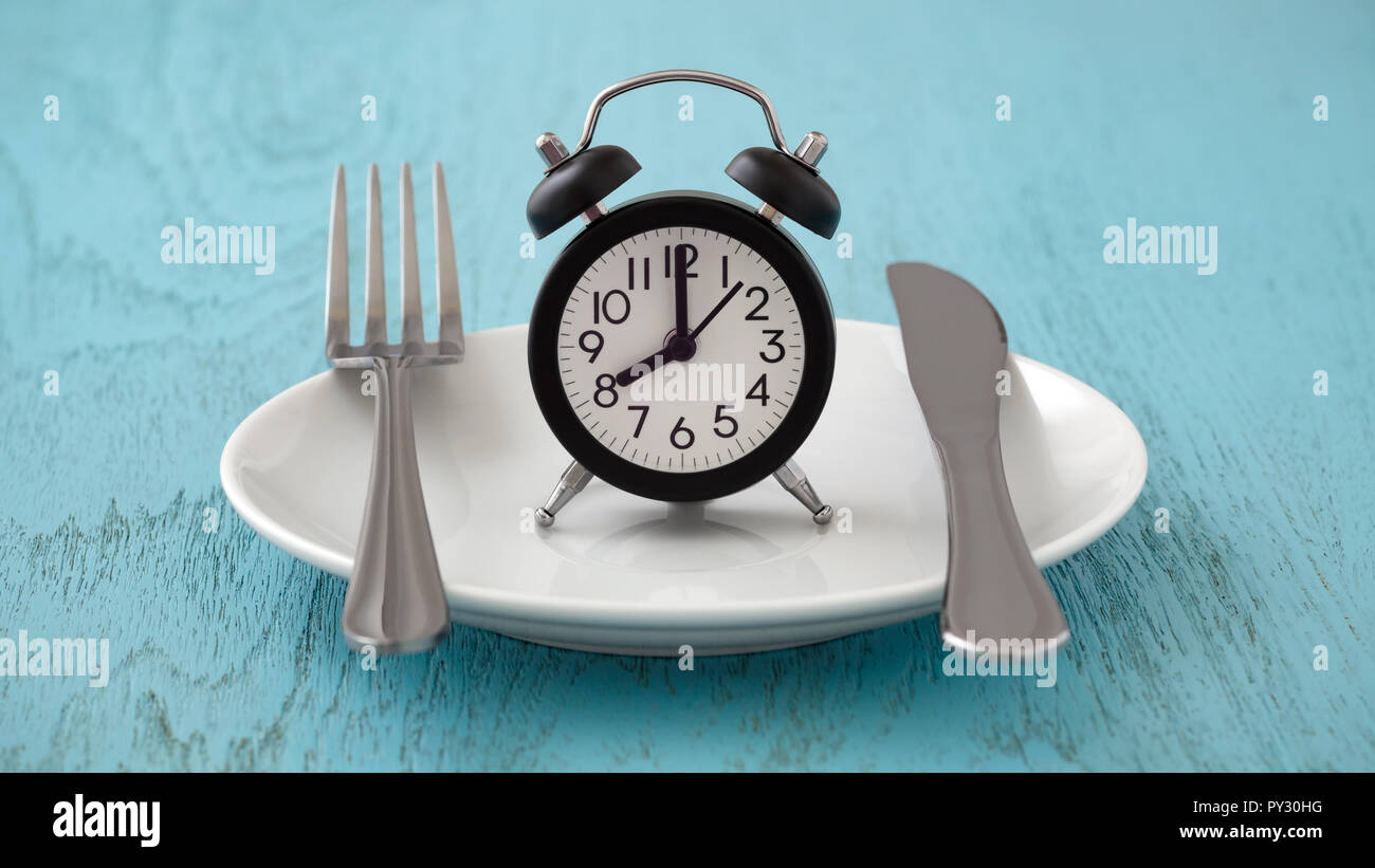 Clock on white plate with fork and knife, intermittent fasting, meal ...