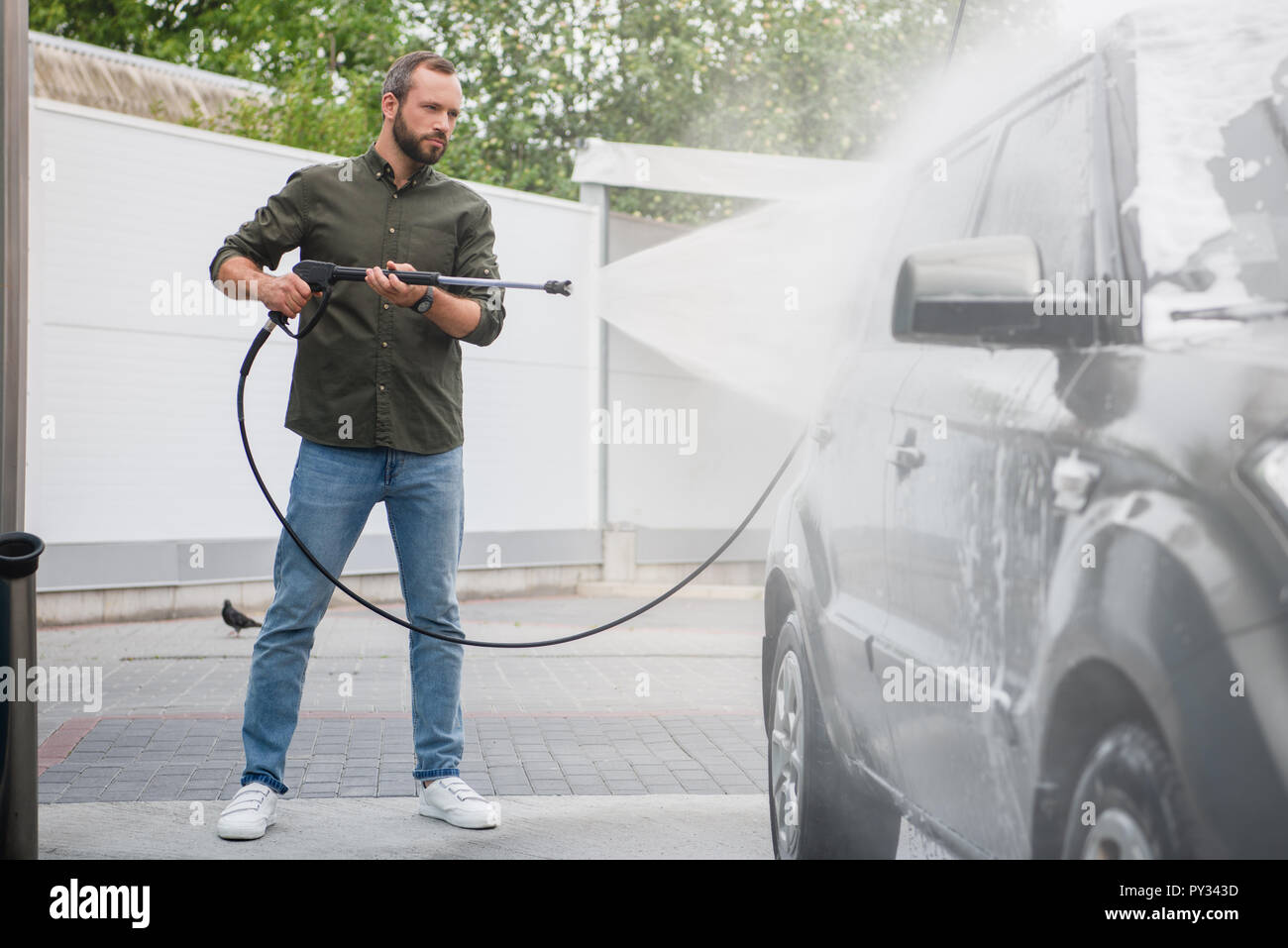 side view of handsome man cleaning car at car wash with high pressure ...