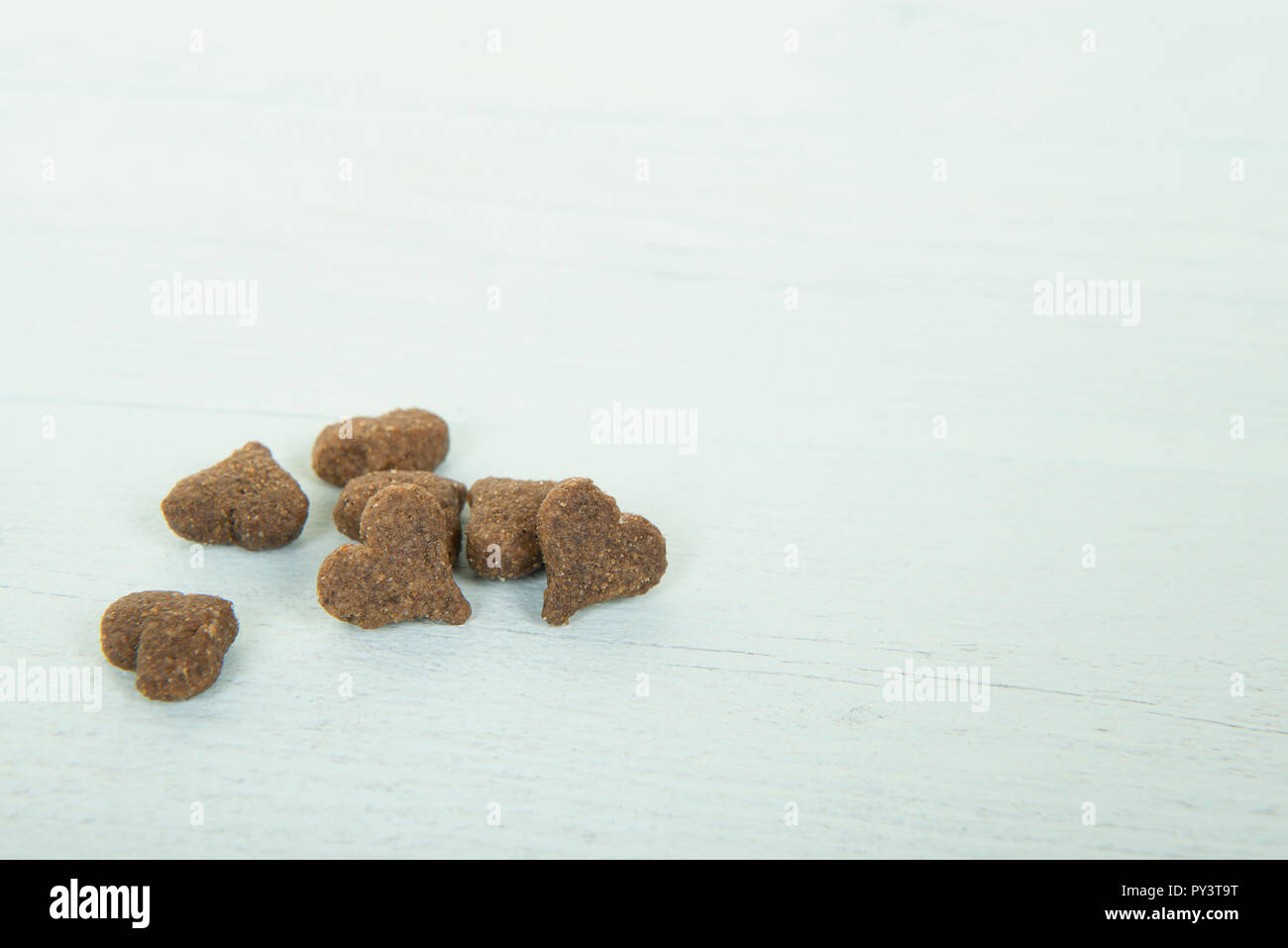 Heart shaped dog or cat kibble seen from above on a light blue wooden ...