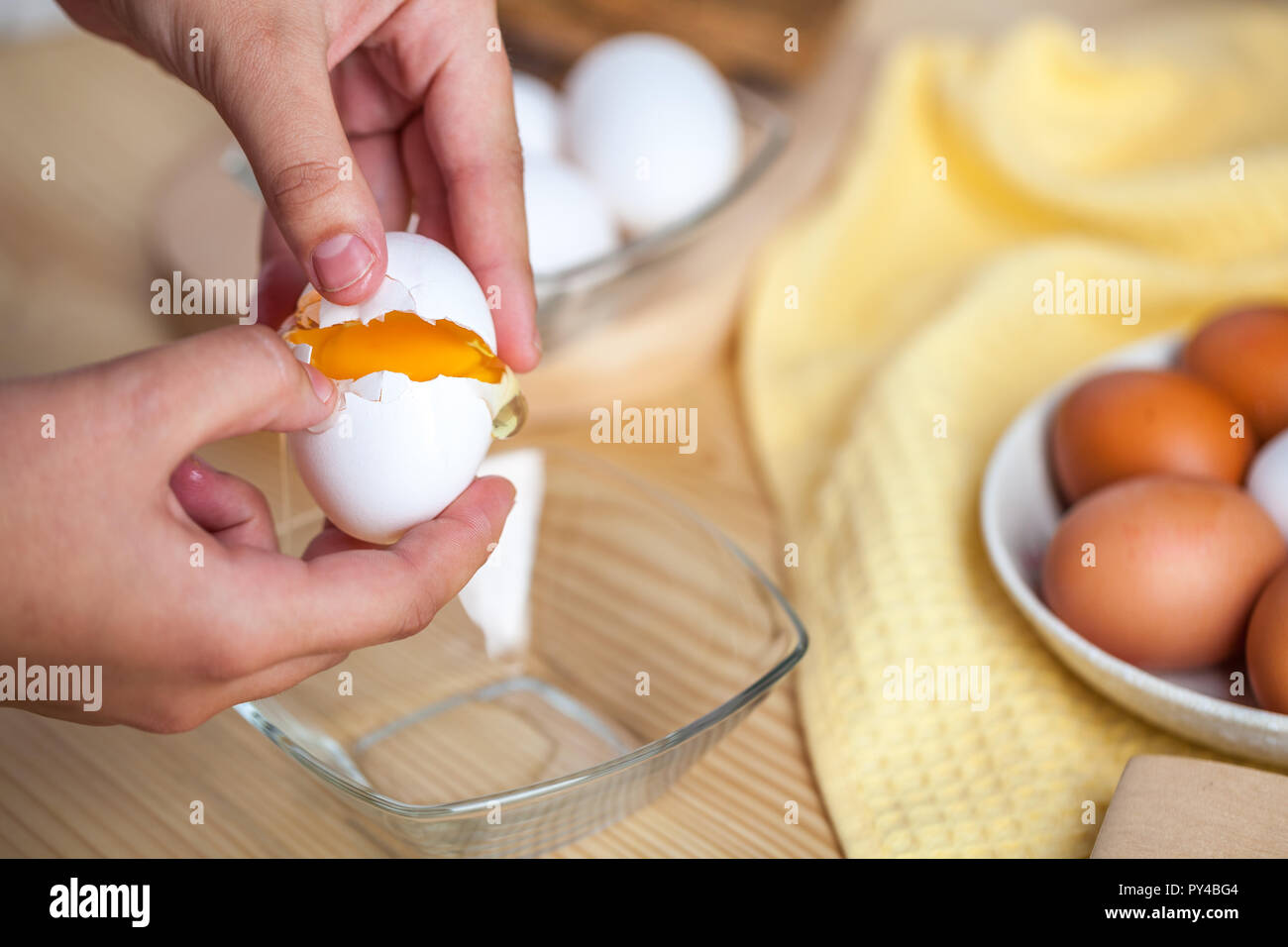 Woman hands breaking an egg to separate egg white and yolks, egg shells at the background Stock ...