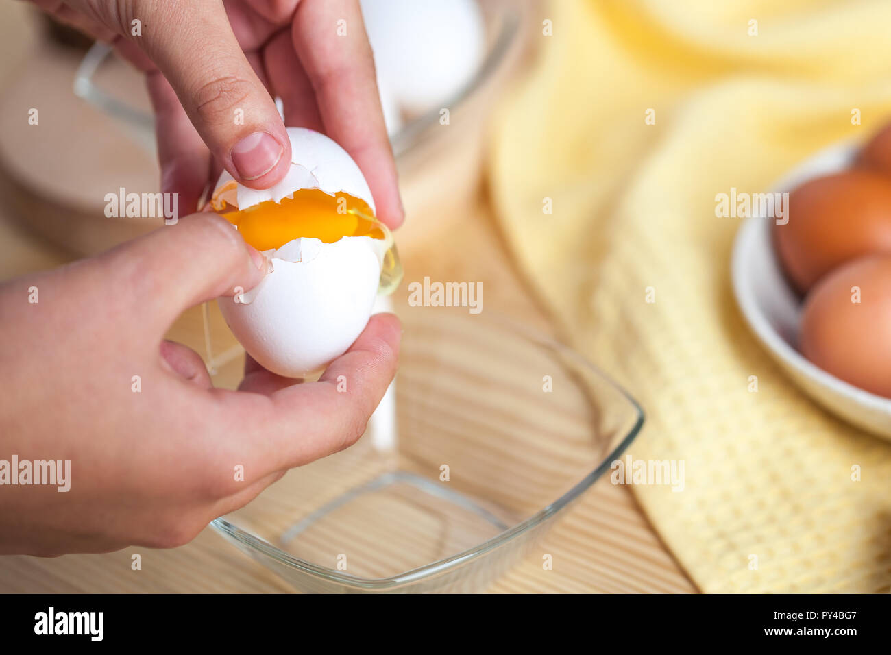 Woman hands breaking an egg to separate egg white and yolks, egg shells at the background Stock ...