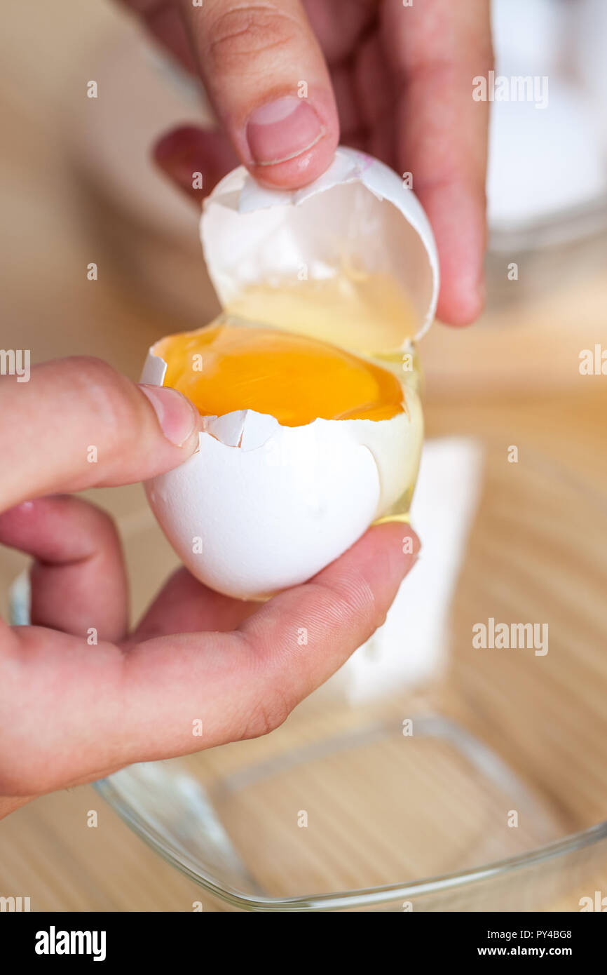 Woman hands breaking an egg to separate egg white and yolks, egg shells at the background Stock ...