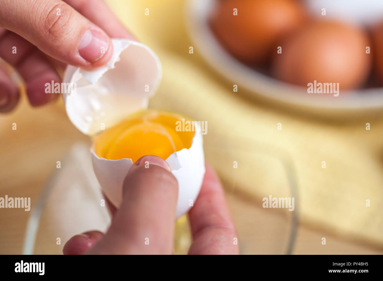 Woman hands breaking an egg to separate egg white and yolks, egg shells at the background Stock ...