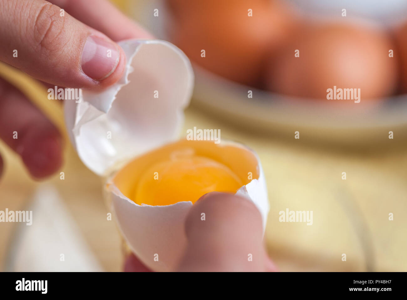 Woman hands breaking an egg to separate egg white and yolks, egg shells at the background Stock ...