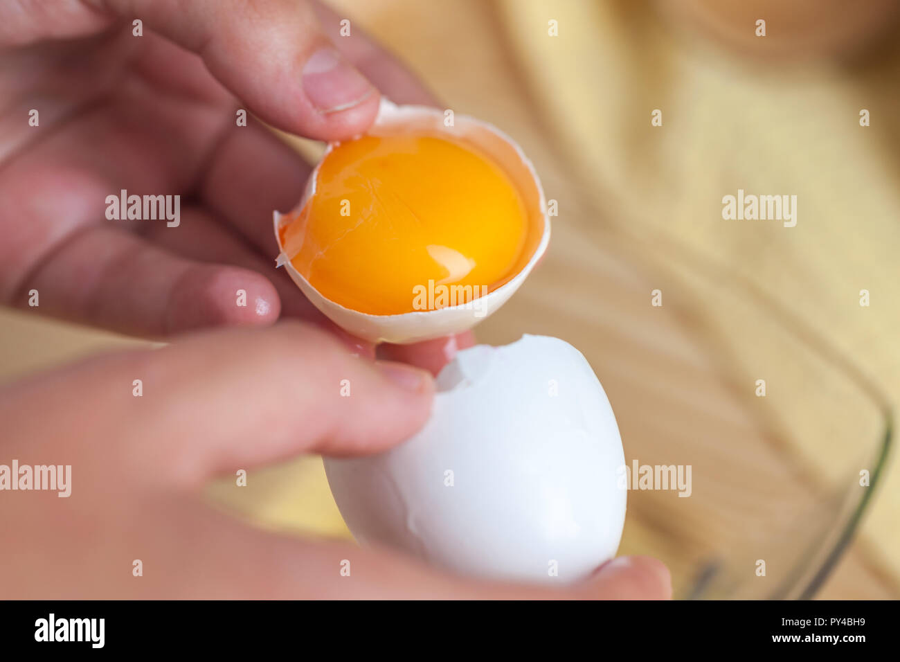 Woman hands breaking an egg to separate egg white and yolks, egg shells at the background Stock ...