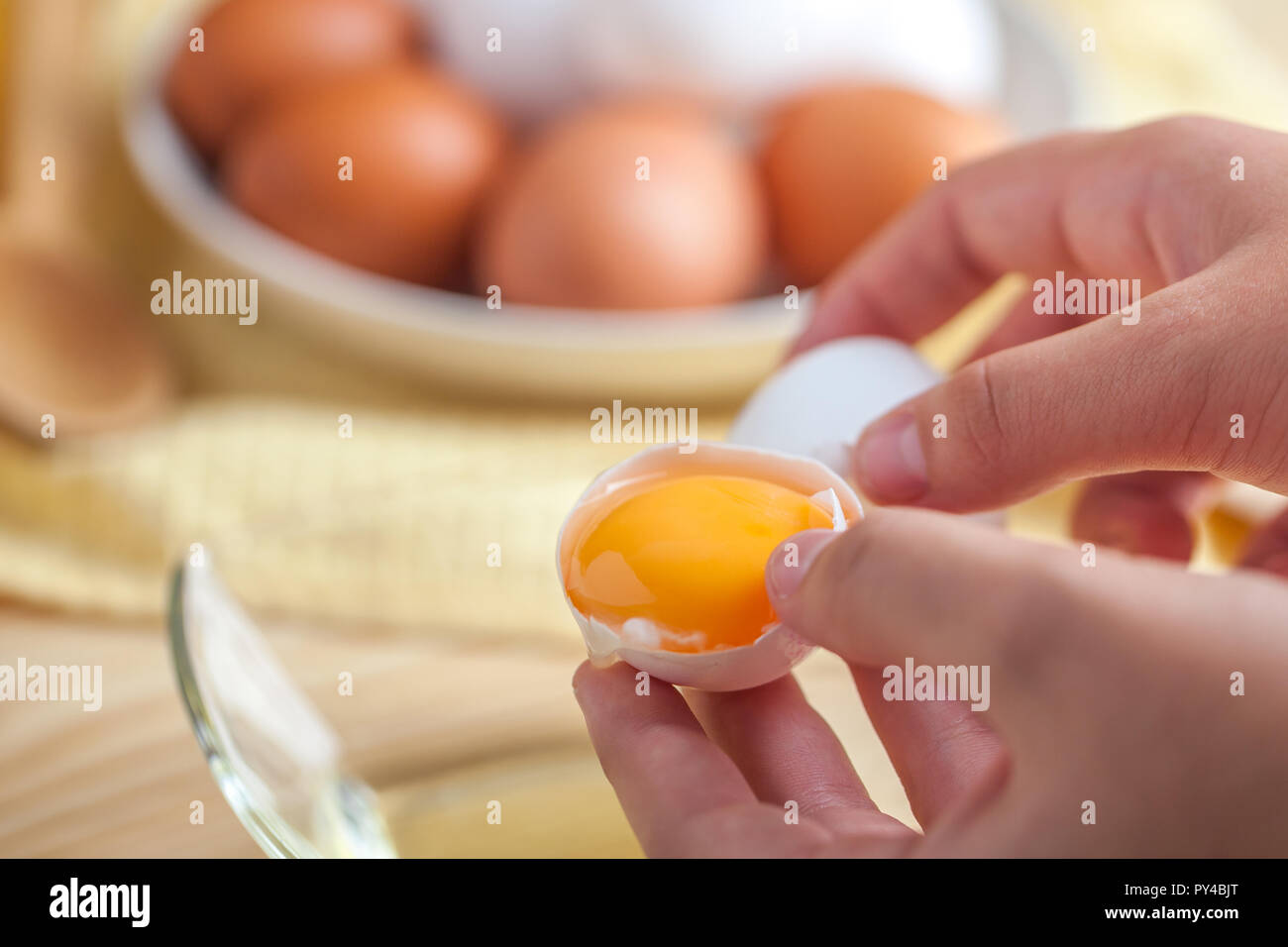 Woman hands breaking an egg to separate egg white and yolks, egg shells at the background Stock ...