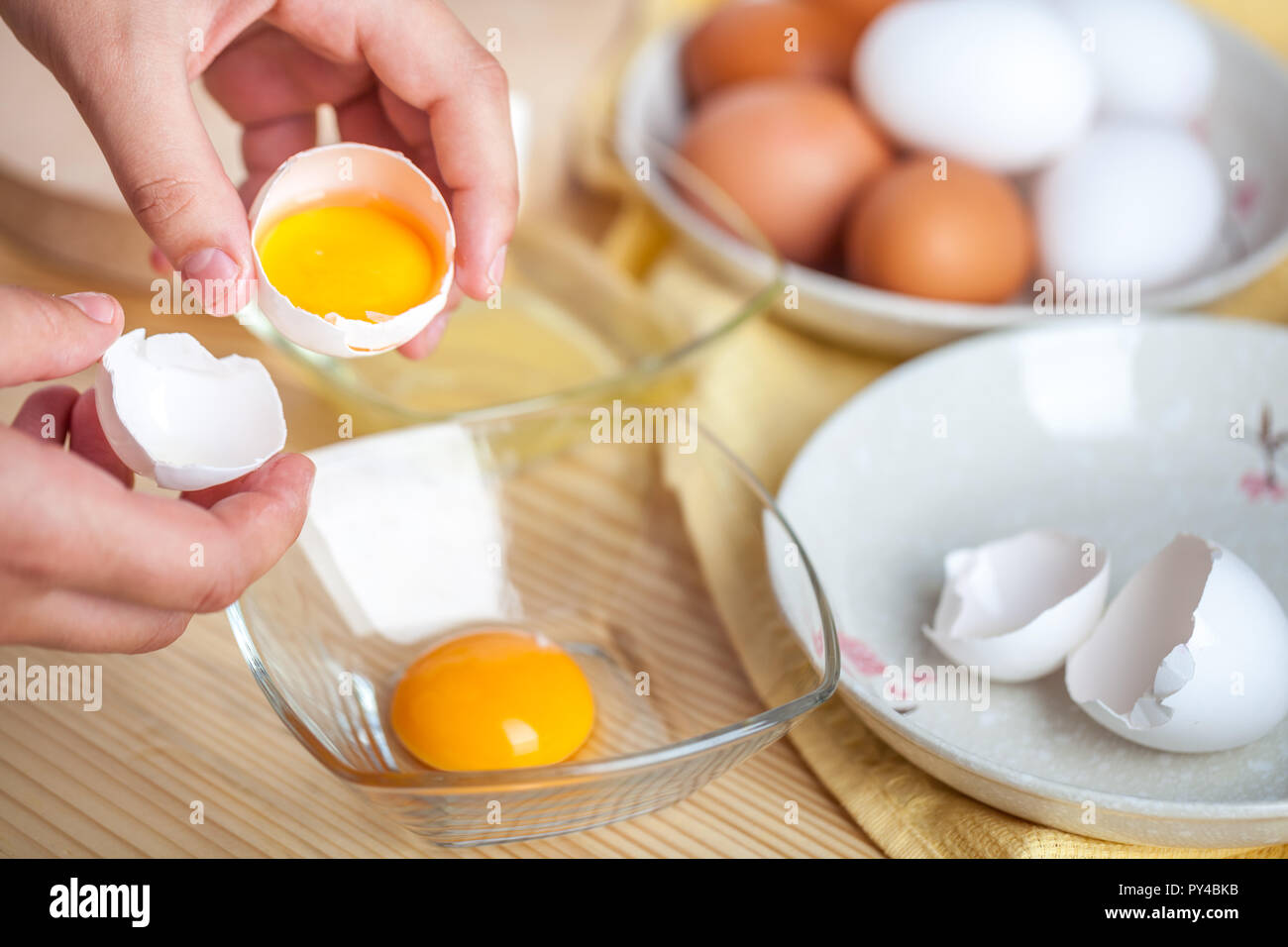 Woman hands breaking an egg to separate egg white and yolks, egg shells at the background Stock ...