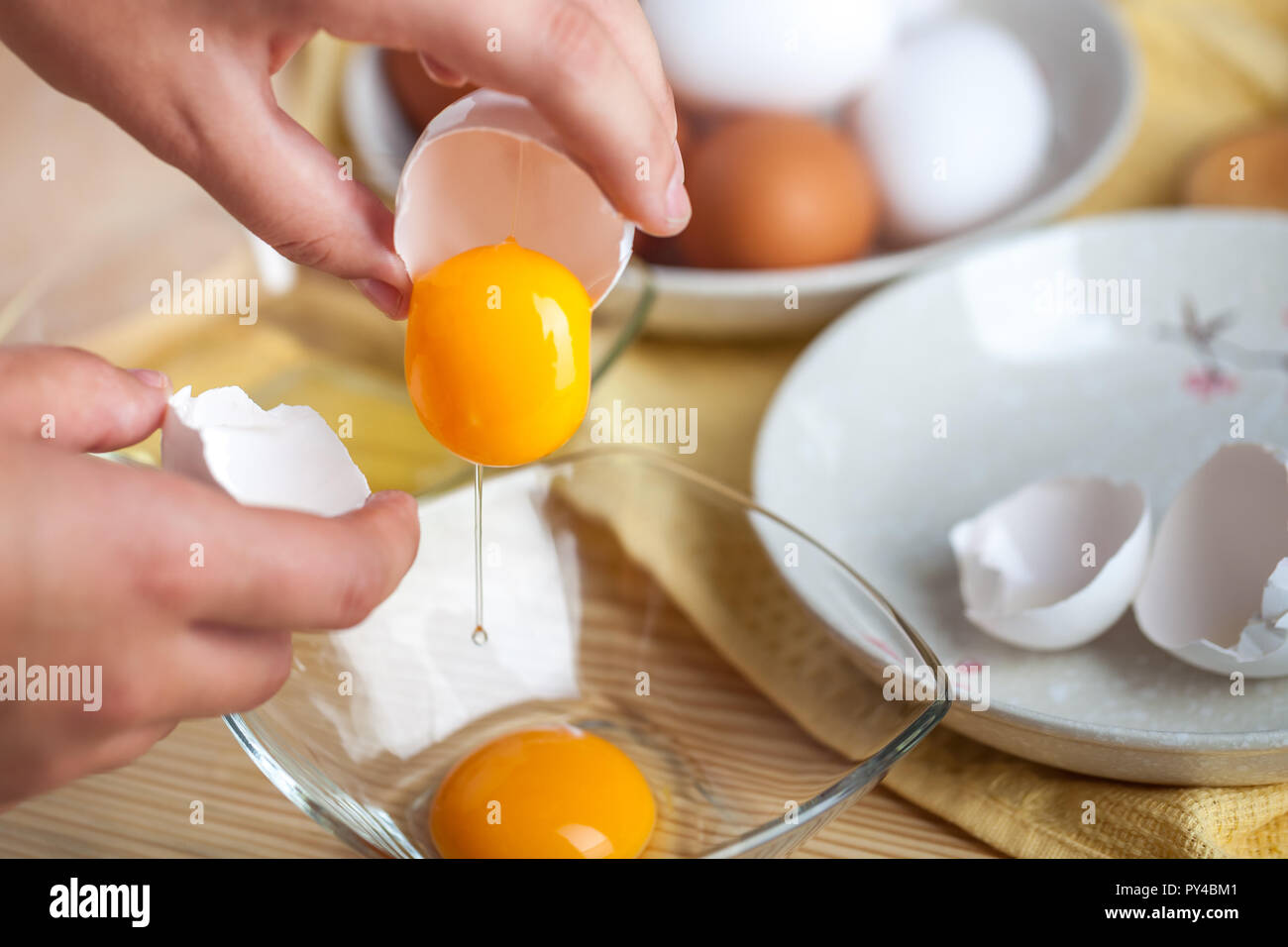 Woman hands breaking an egg to separate egg white and yolks, egg shells at the background Stock ...