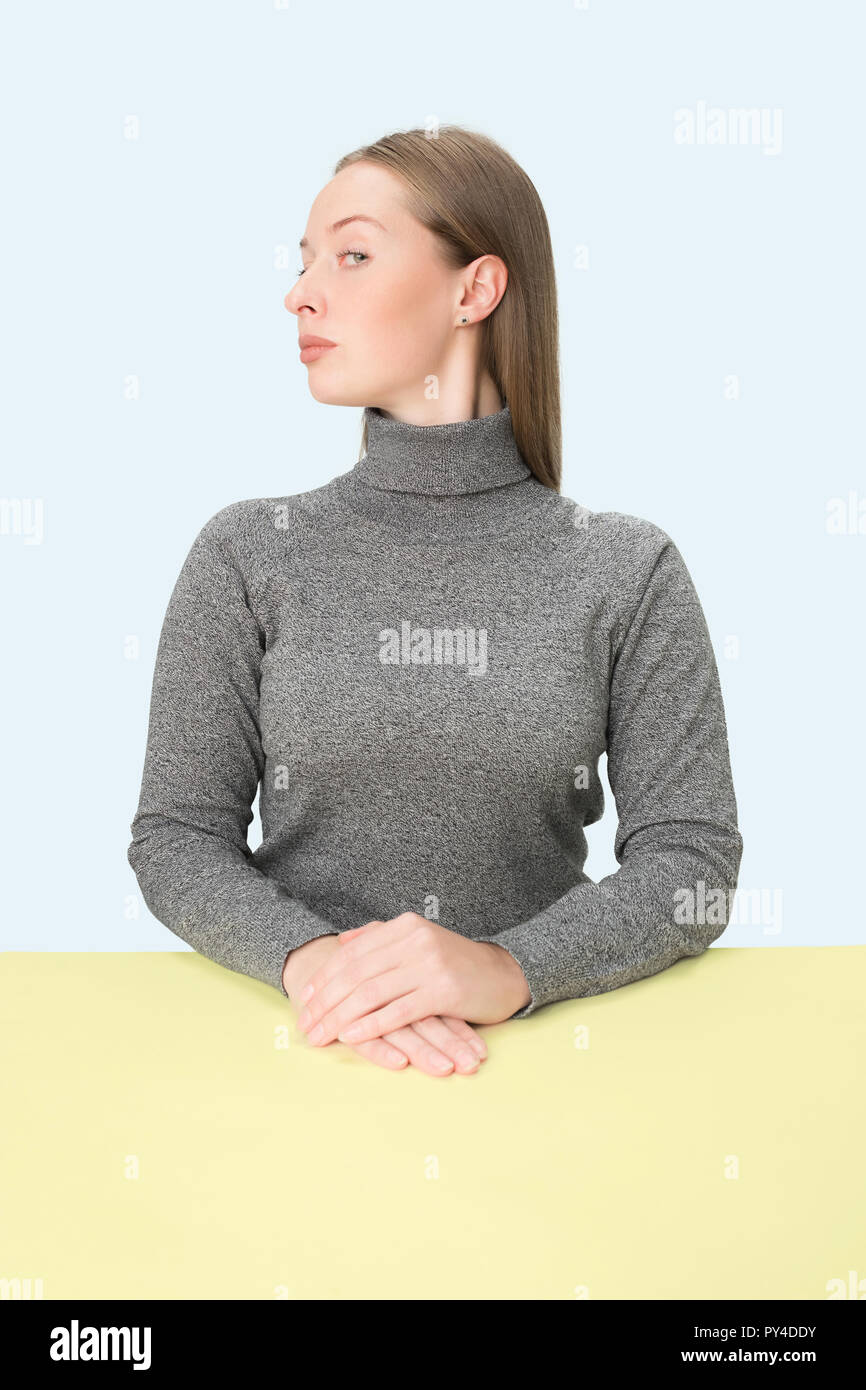 Serious business woman sitting at table on a pink studio background ...