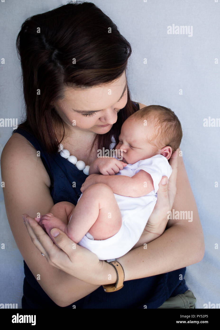Mother holding sleeping newborn baby close to her chest up looking down ...