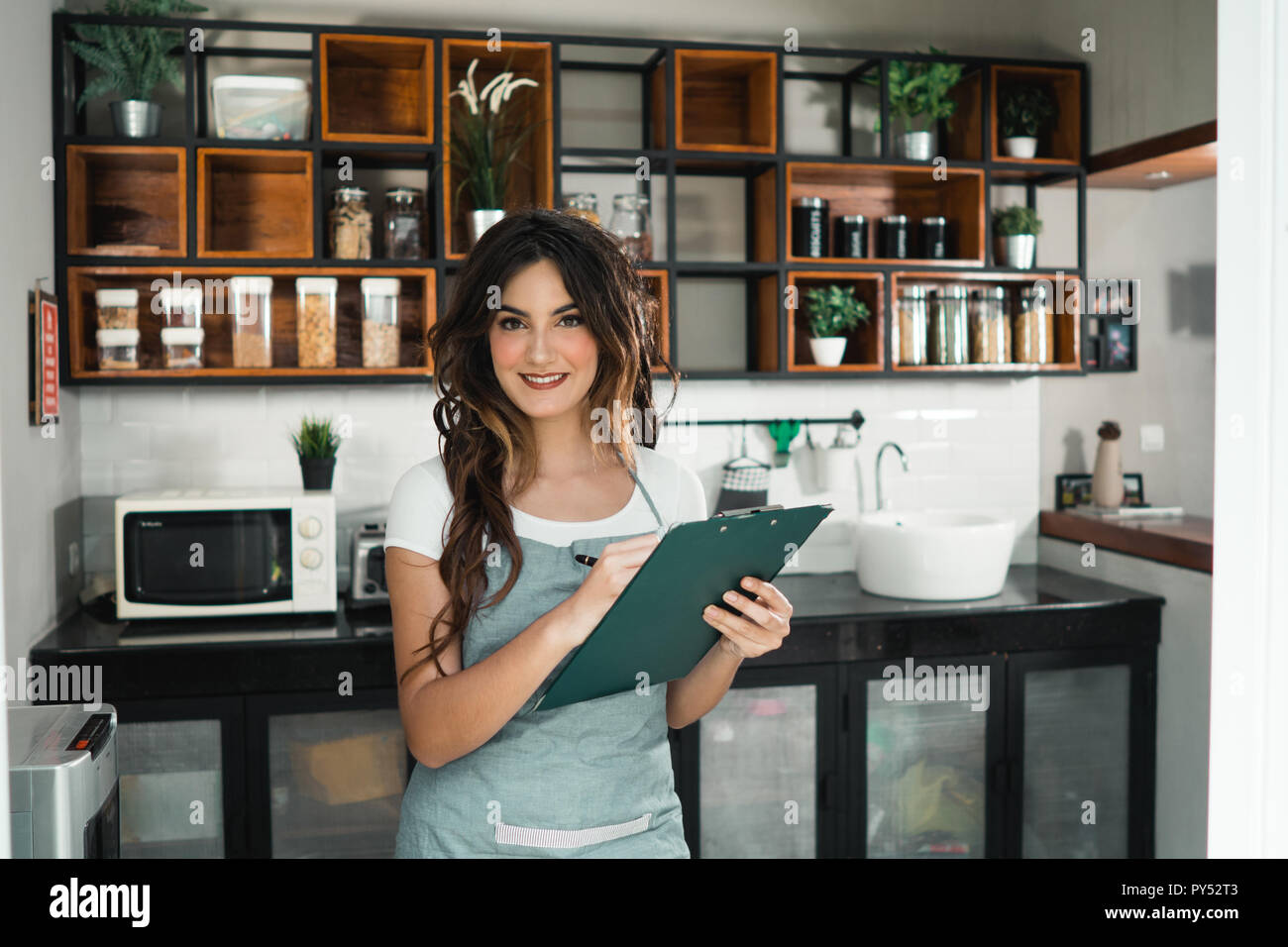 happy young female cafe worker working in a coffee shop writing on a ...