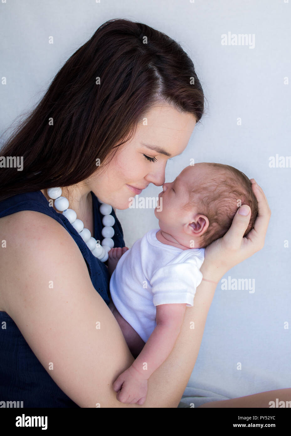 Mother holding newborn baby face to face touching her nose to the baby ...