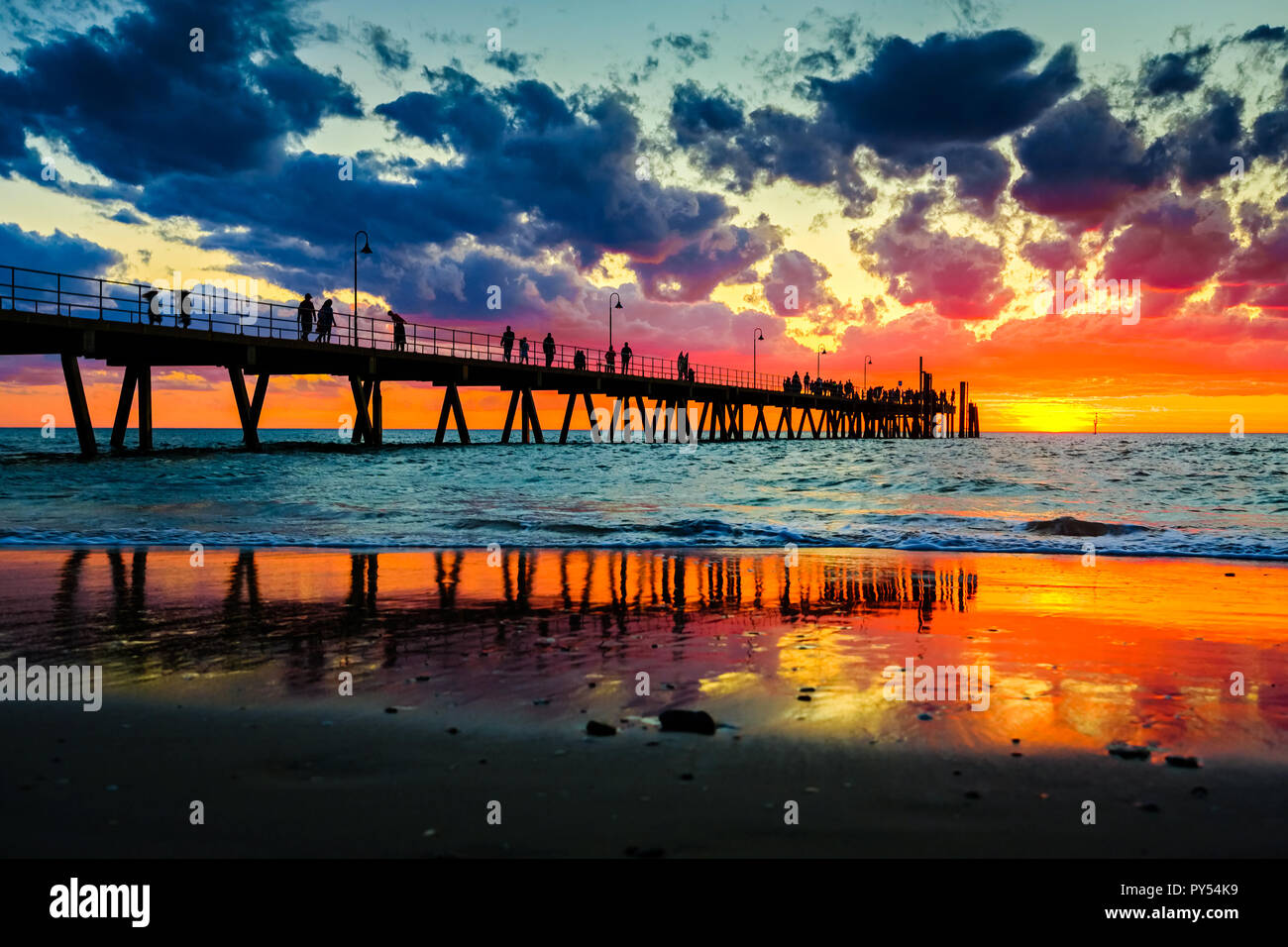 People stroll on Glenelg jetty at sunset sky splashed with colourful ...