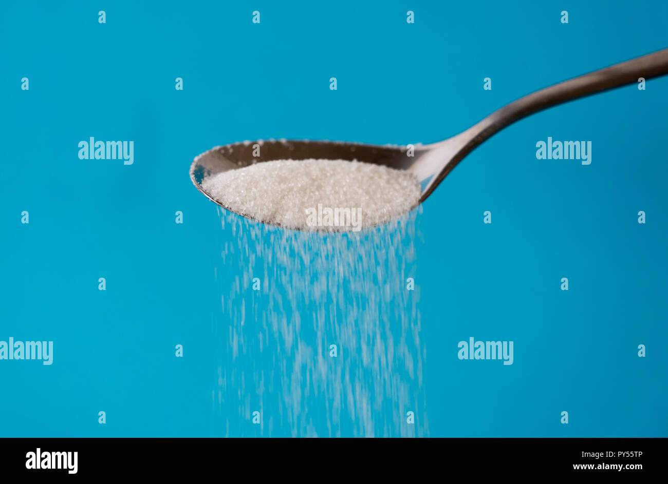 Sugar being pour from a spoon in a stream isolated on blue background ...
