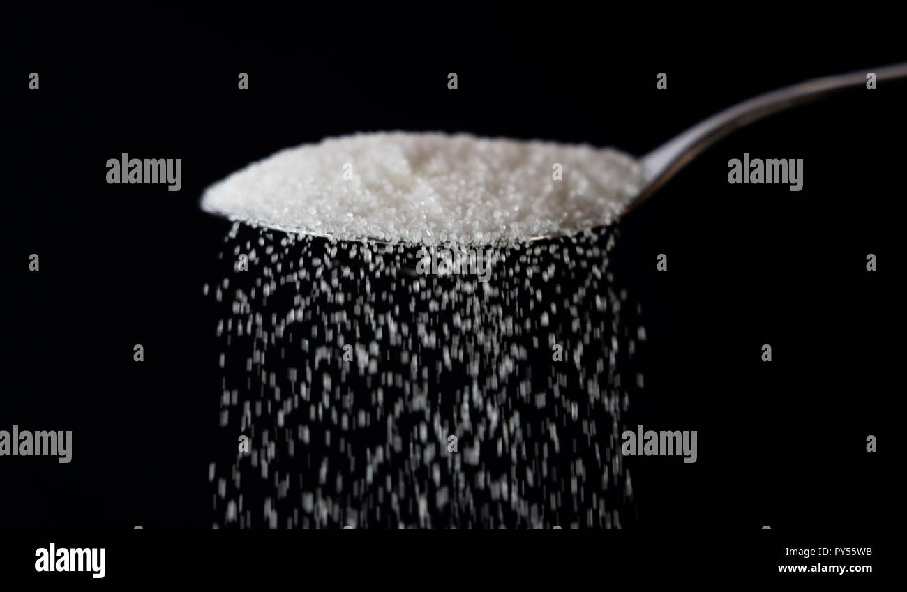 Sugar being pour from a spoon in a stream isolated on black dark ...