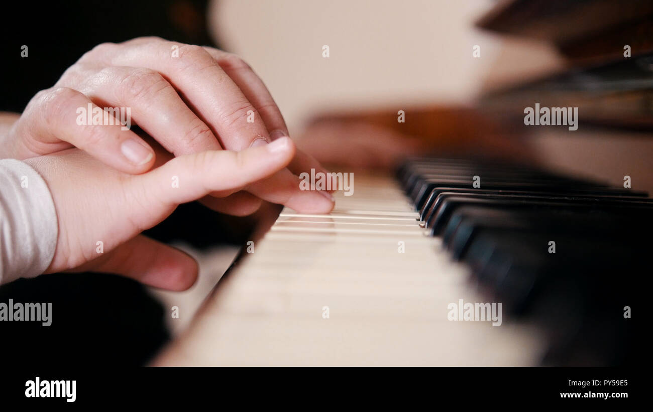 An old teacher teaching little girl how to play piano. Touching hands ...