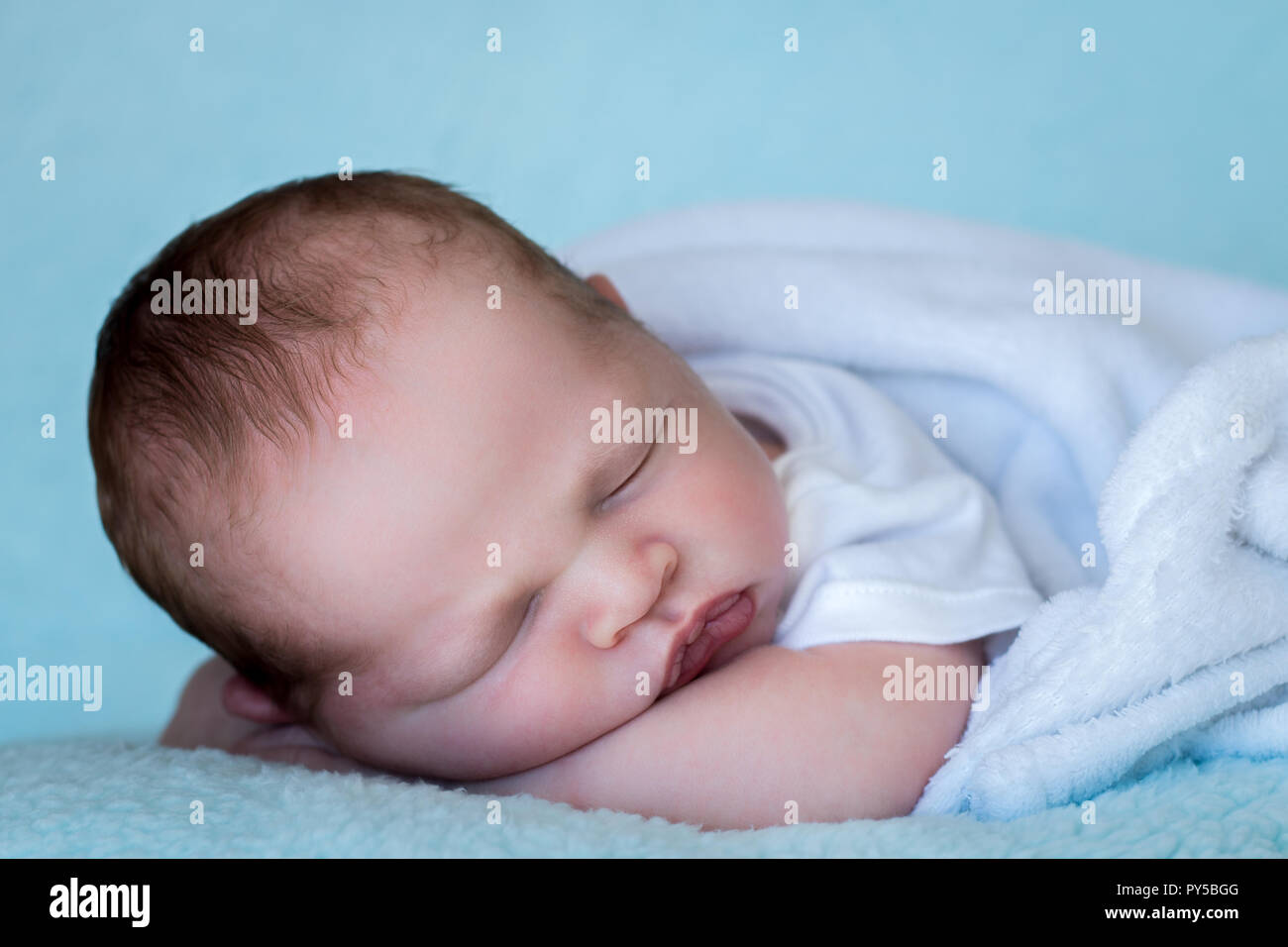 Newborn baby sleeping resting his chin on his arms facing forward close ...