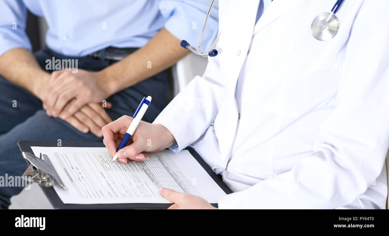 Female doctor holding application form while consulting man patient in ...